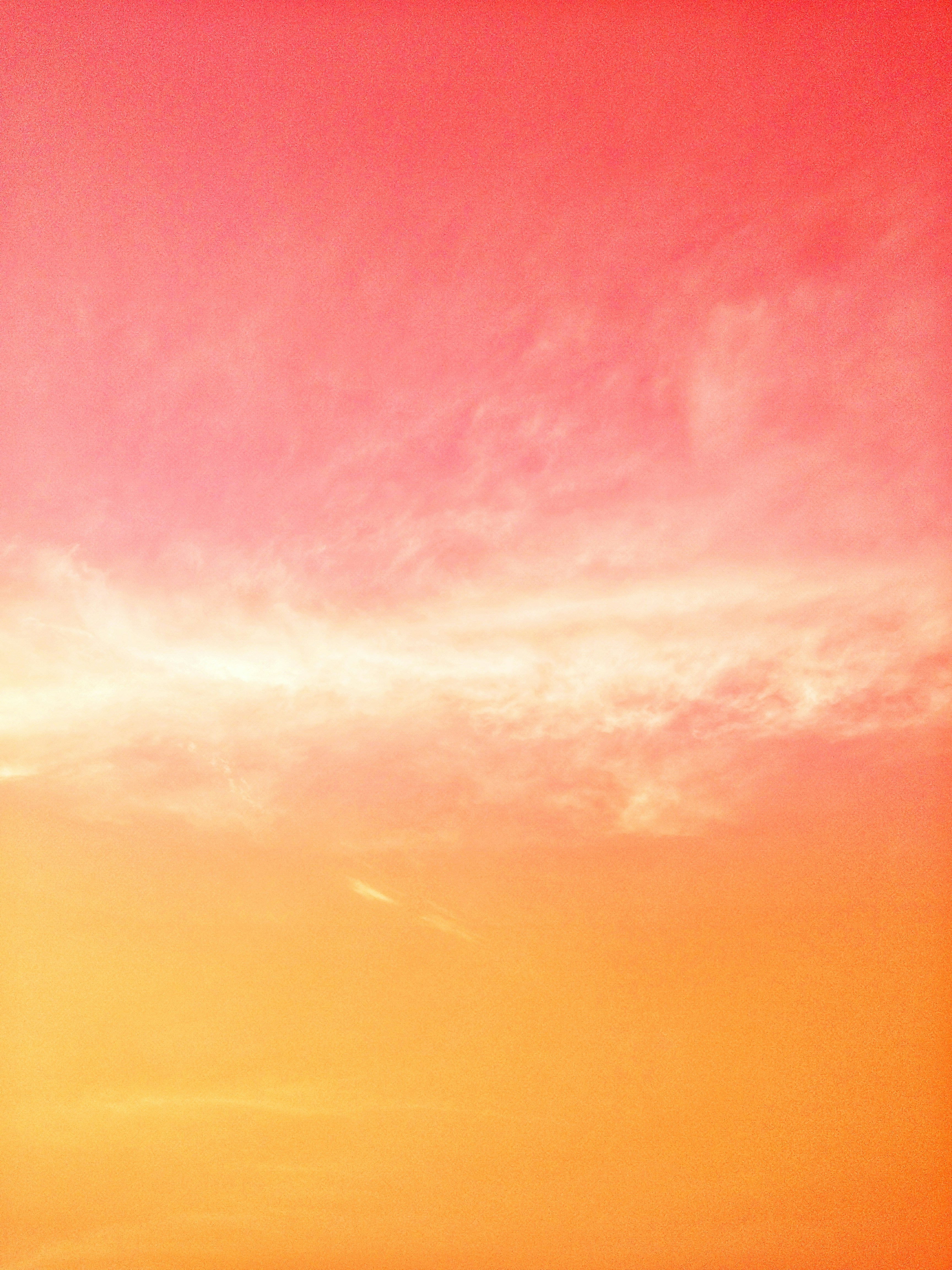 Vibrant gradient of pink and orange hues blending seamlessly in the evening sky, showcasing wispy clouds. 
