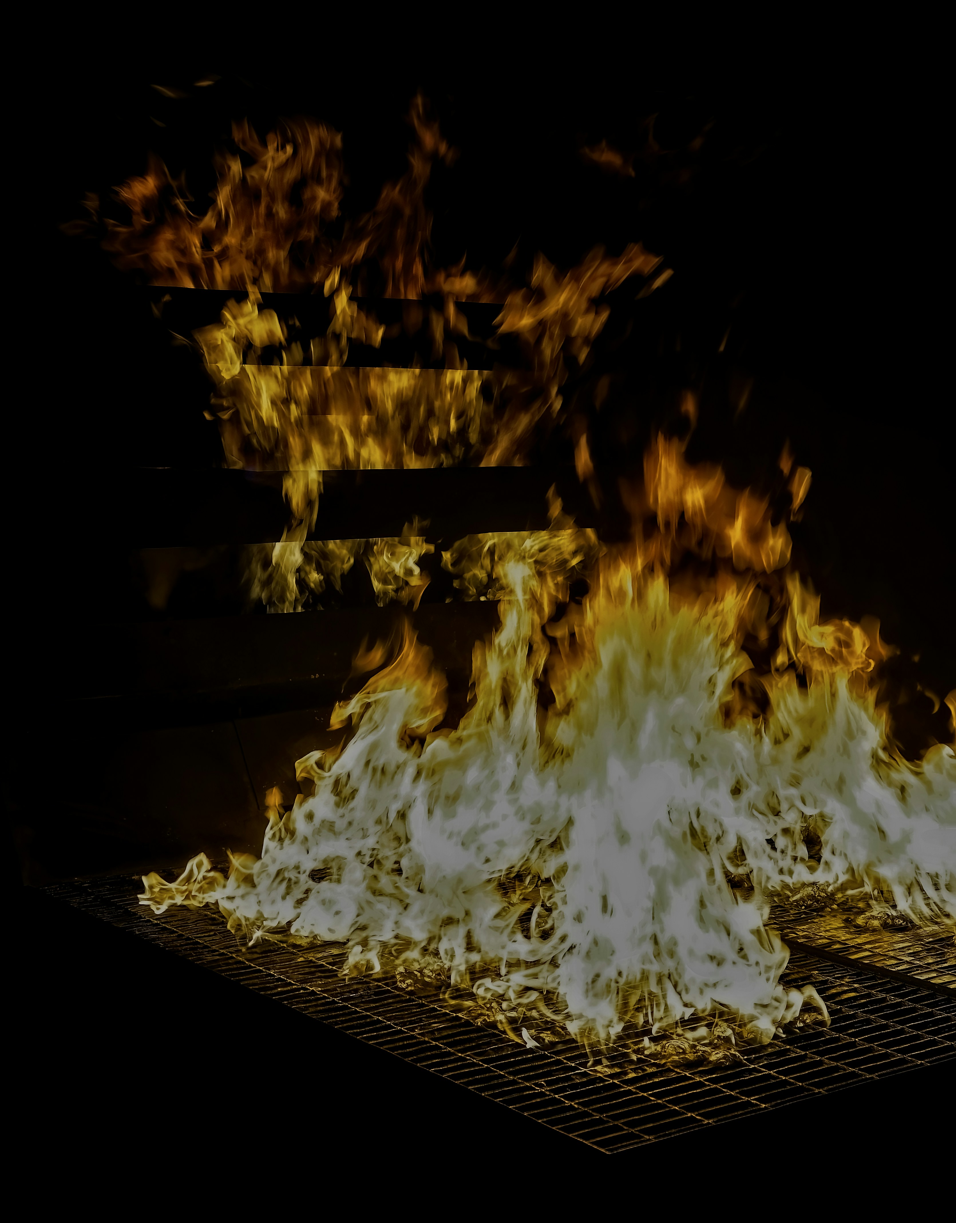 Intense flames engulf a metal grate in a dark setting.