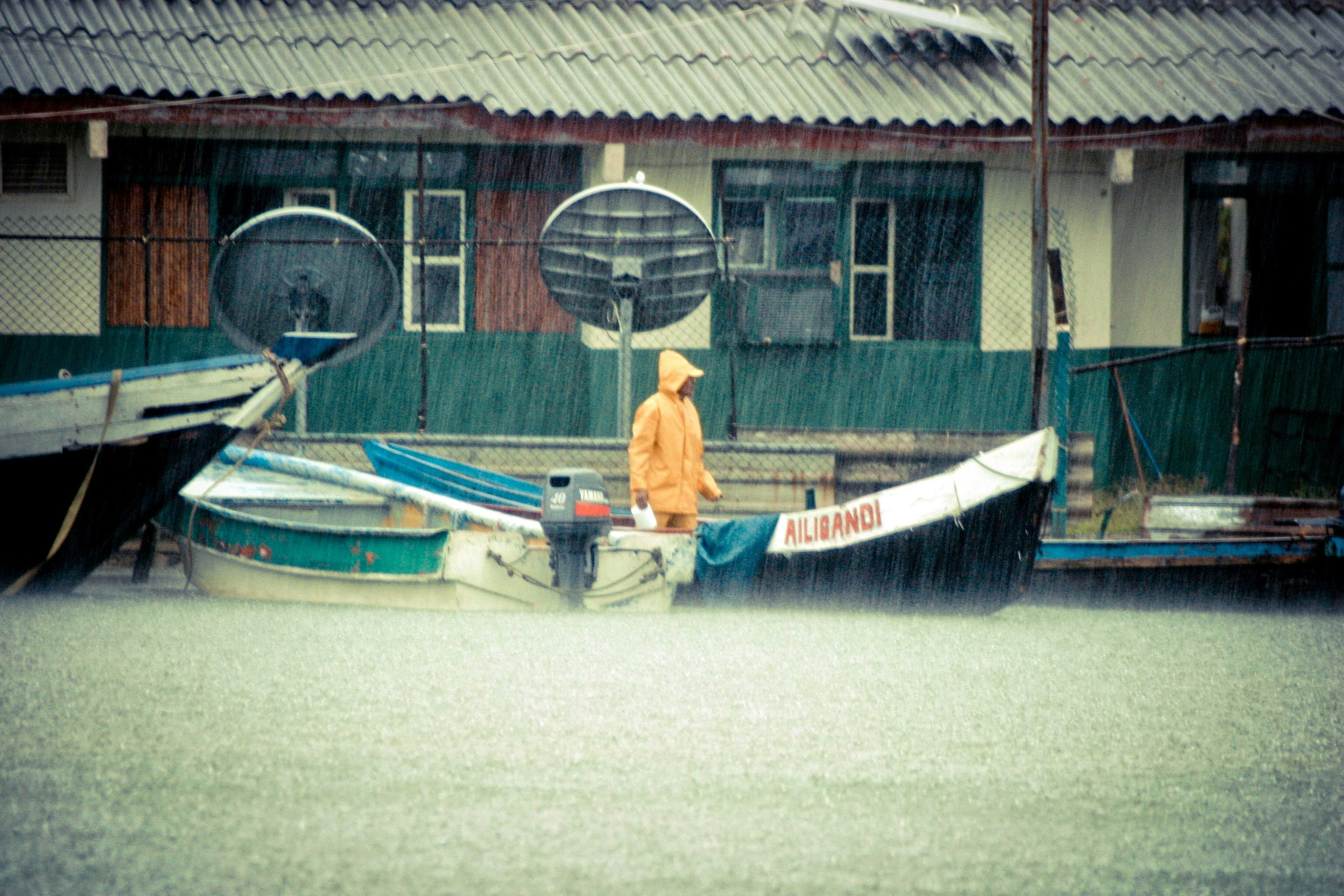 Orange-Robed Mariner in a Rain-Swept Harbor Among Boats and Satellite Dishes