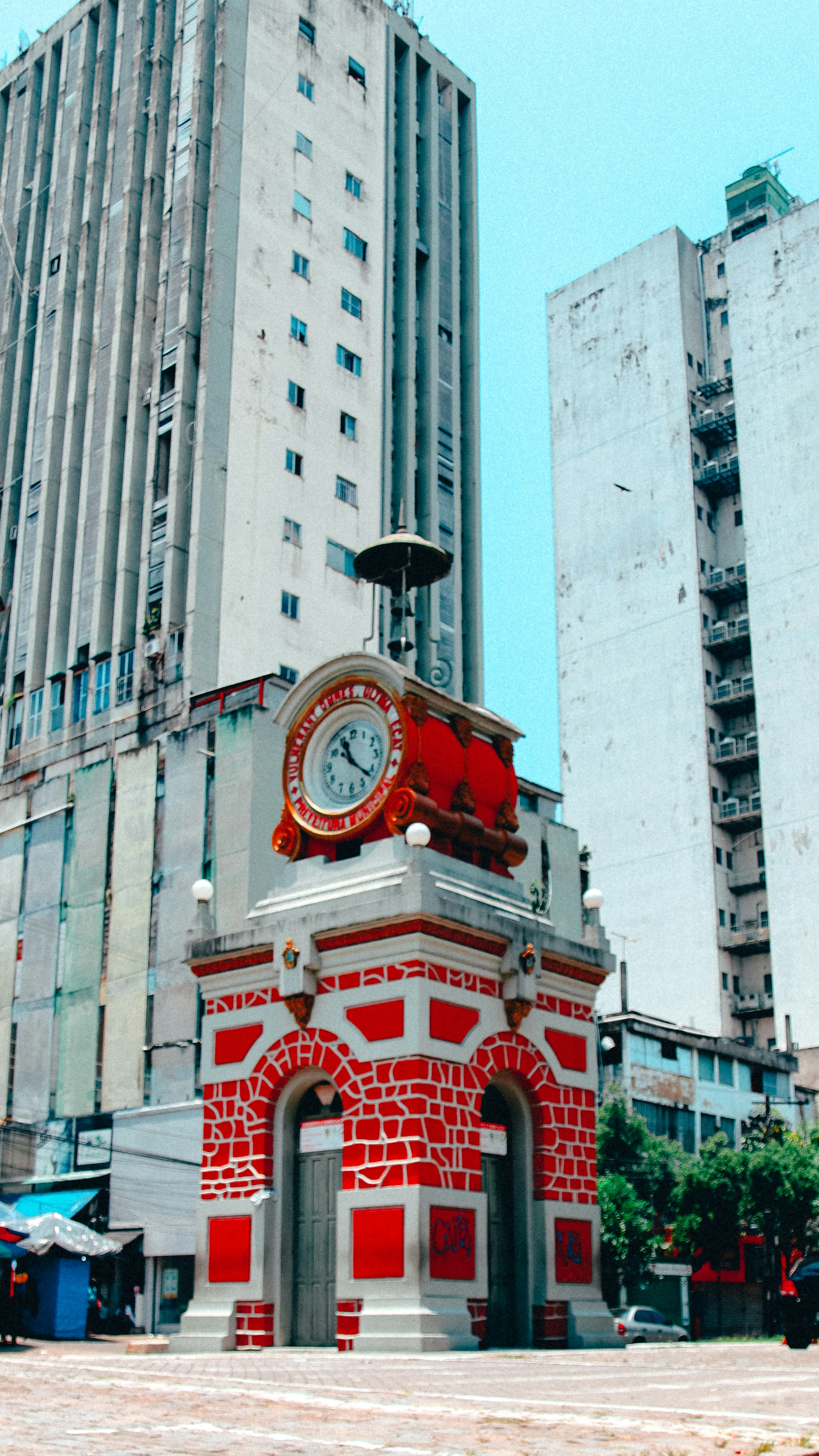 Ornate red and white clock tower contrasts with tall modern buildings under a clear blue sky.