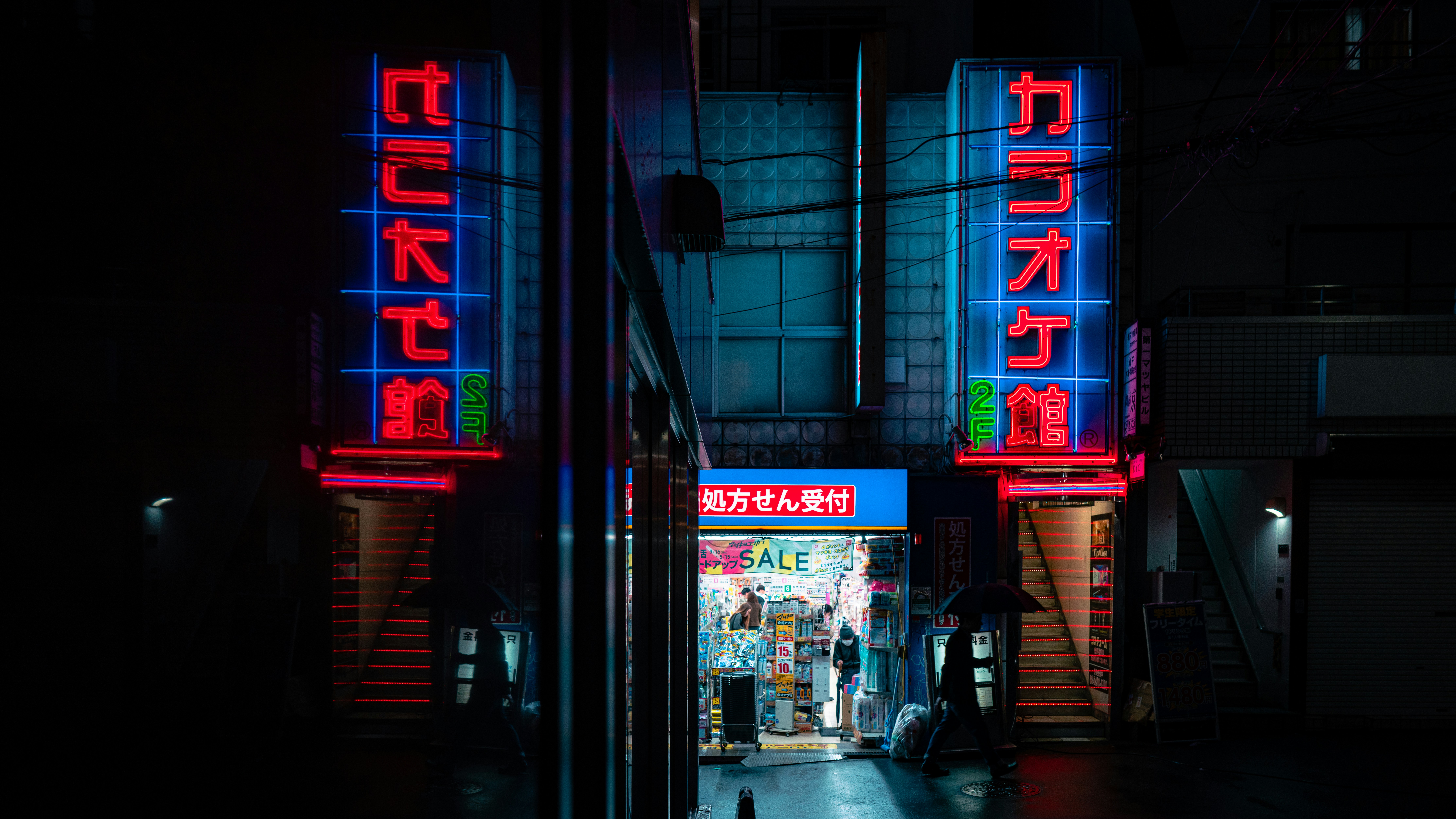 Vibrant neon signs illuminate a karaoke parlor entrance, showcasing a bustling atmosphere. The glow reflects off nearby surfaces, enhancing the urban night scene.
