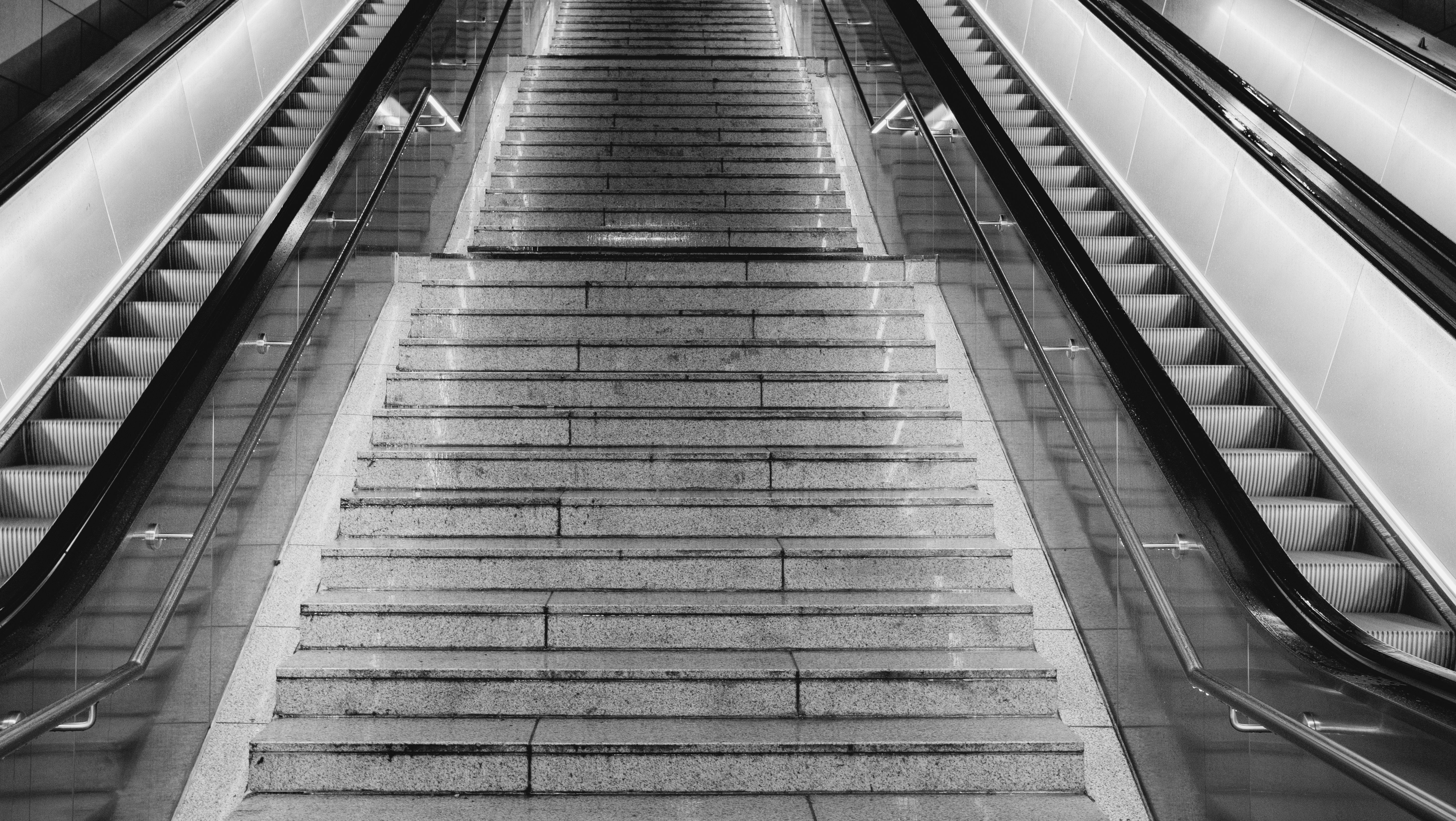 Black and white view of a modern staircase flanked by escalators, emphasizing symmetry and perspective.
