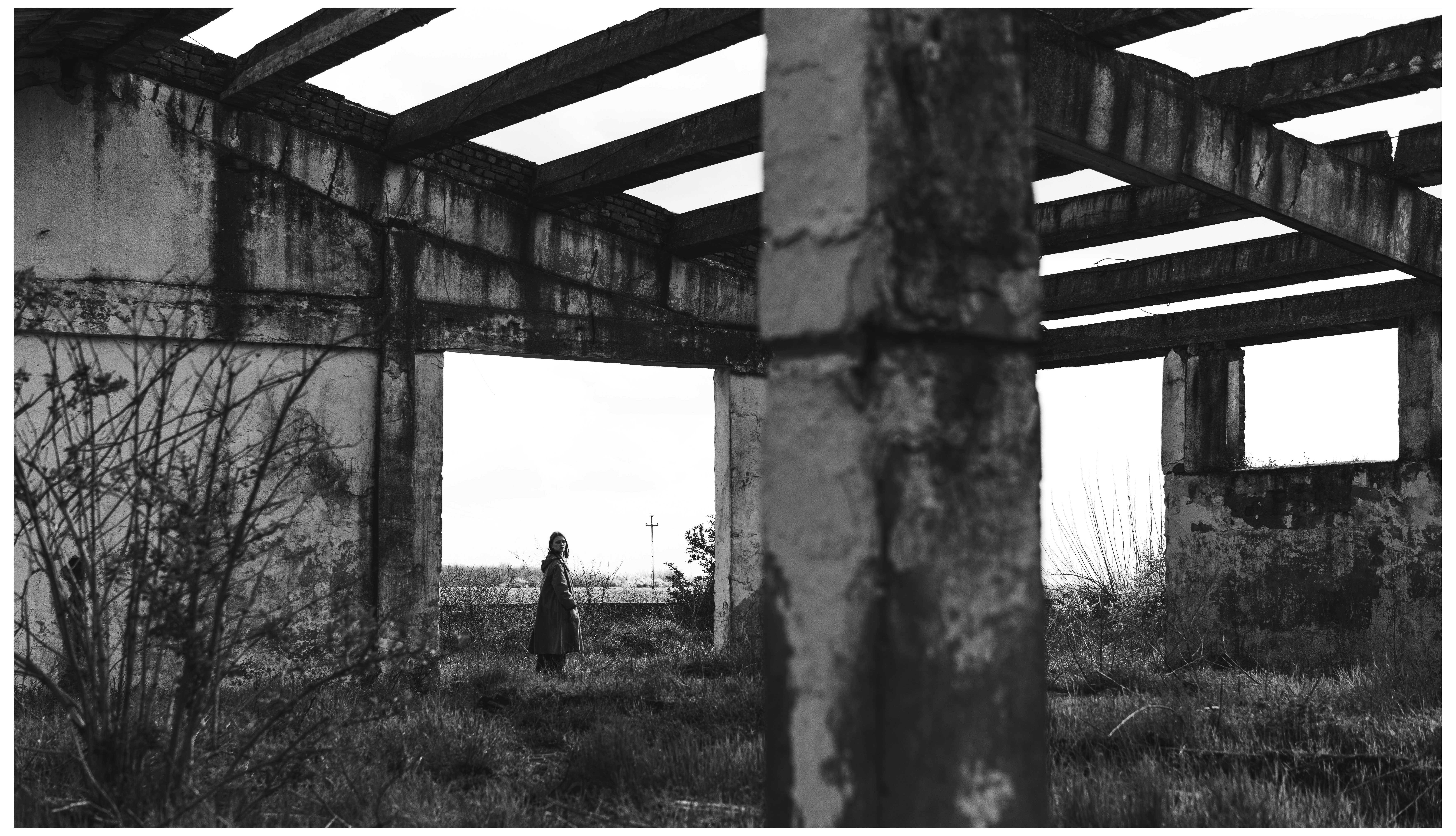 Silhouette of a person walking under a dilapidated concrete structure with geometric shadows.