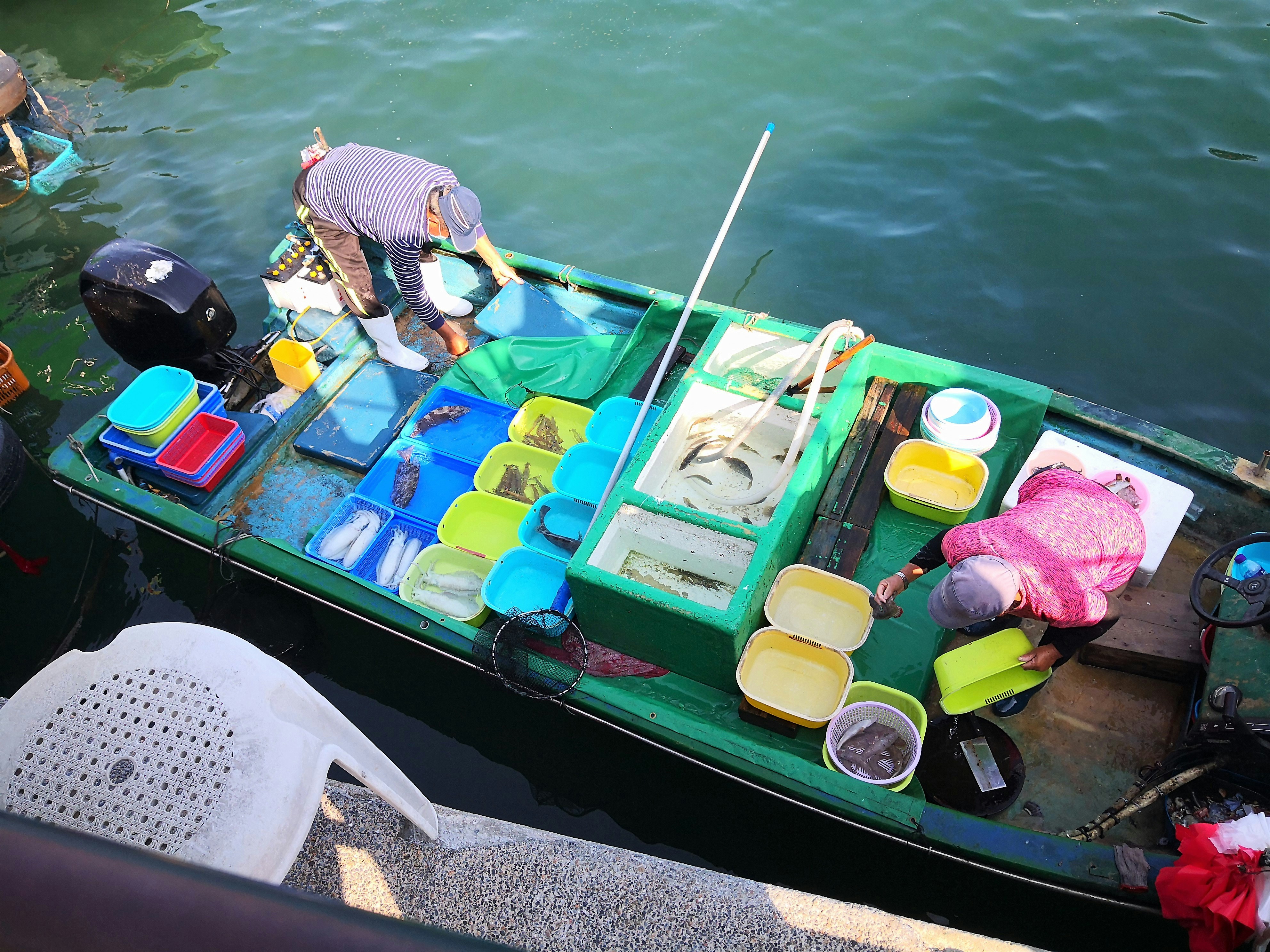 Fishermen sorting their catch on a vibrant boat filled with colorful containers, surrounded by tranquil waters.