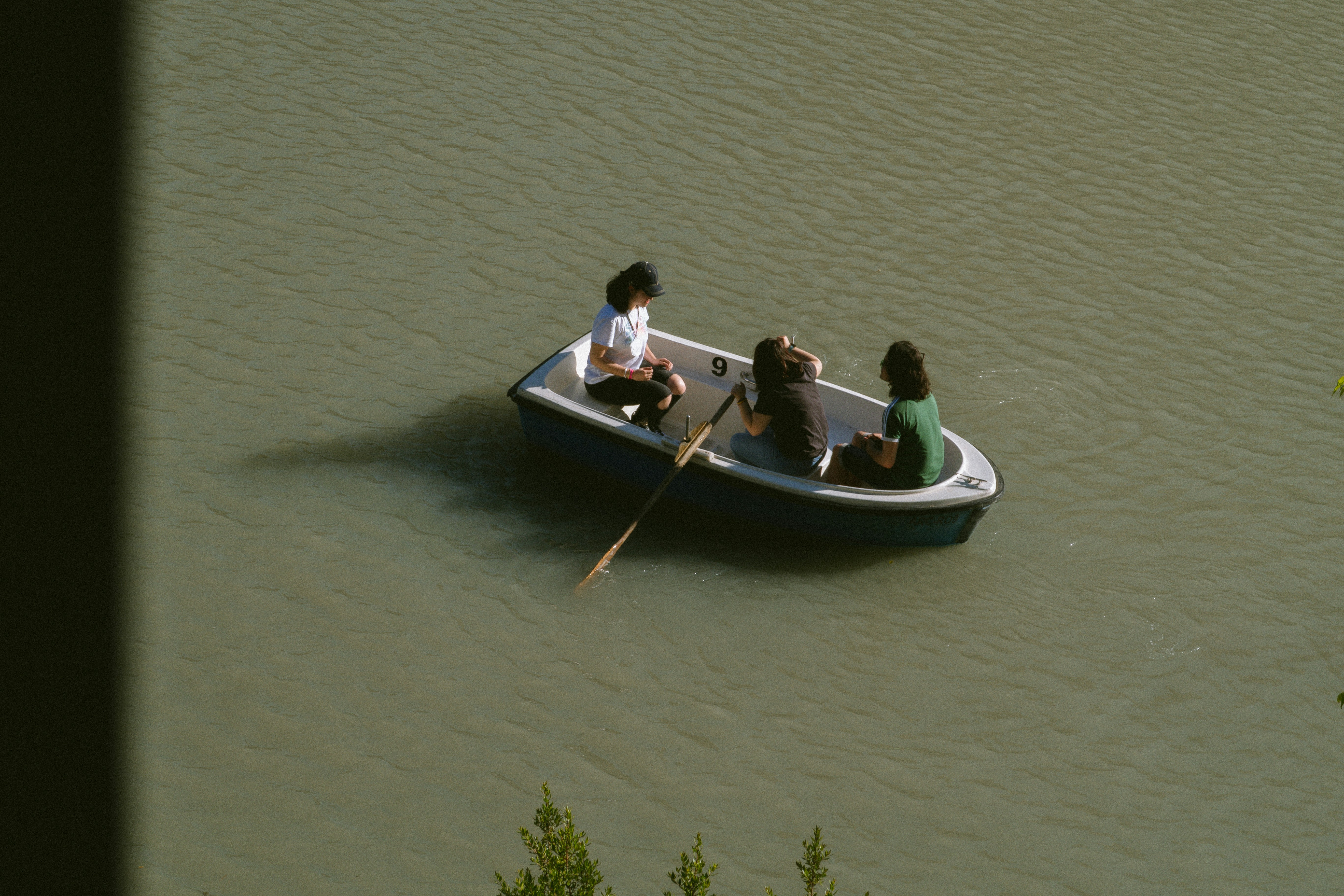 Three people in a small rowboat on calm, greenish water.