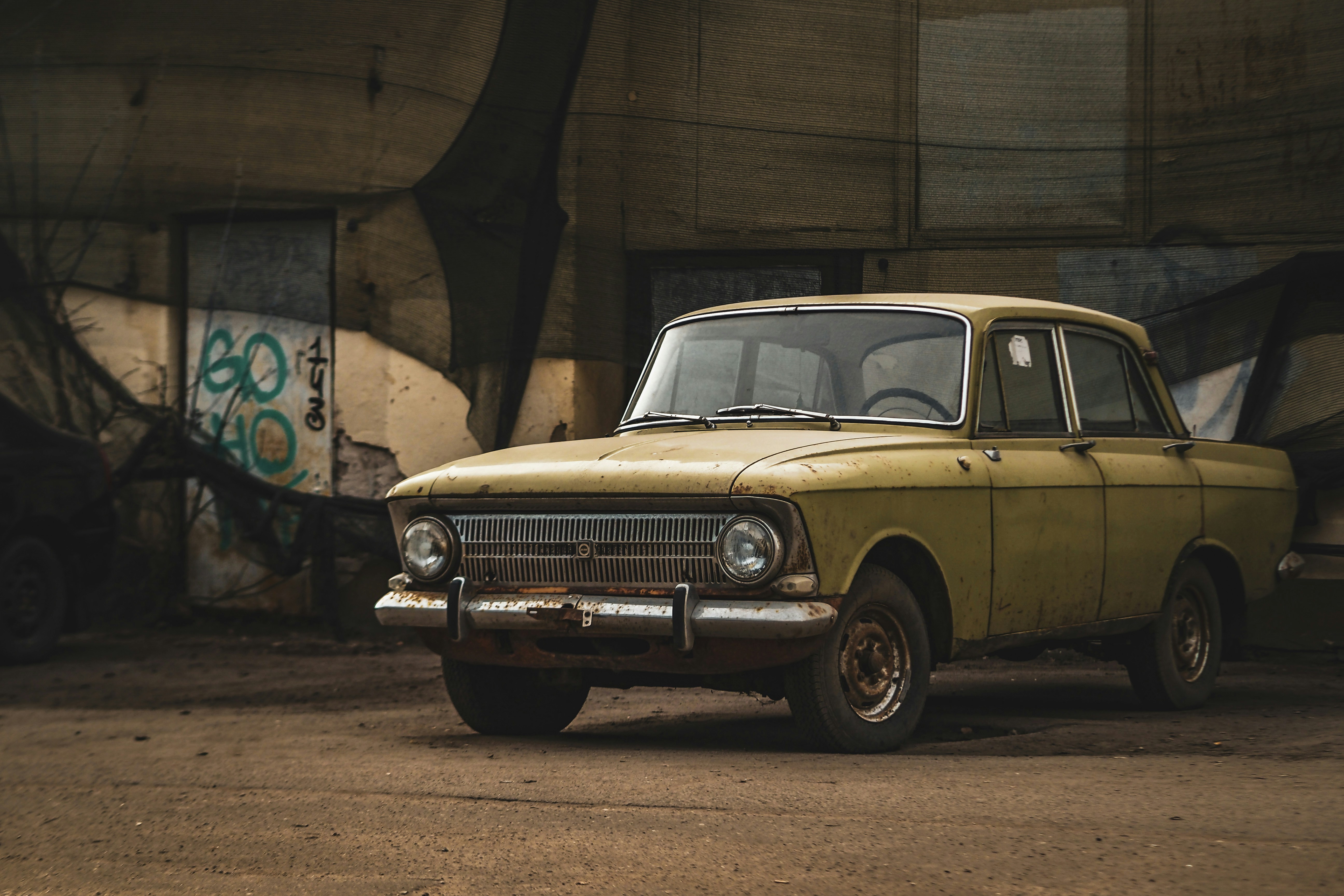 Vintage yellow sedan parked in an abandoned industrial area, showcasing weathered paint and nostalgic charm.