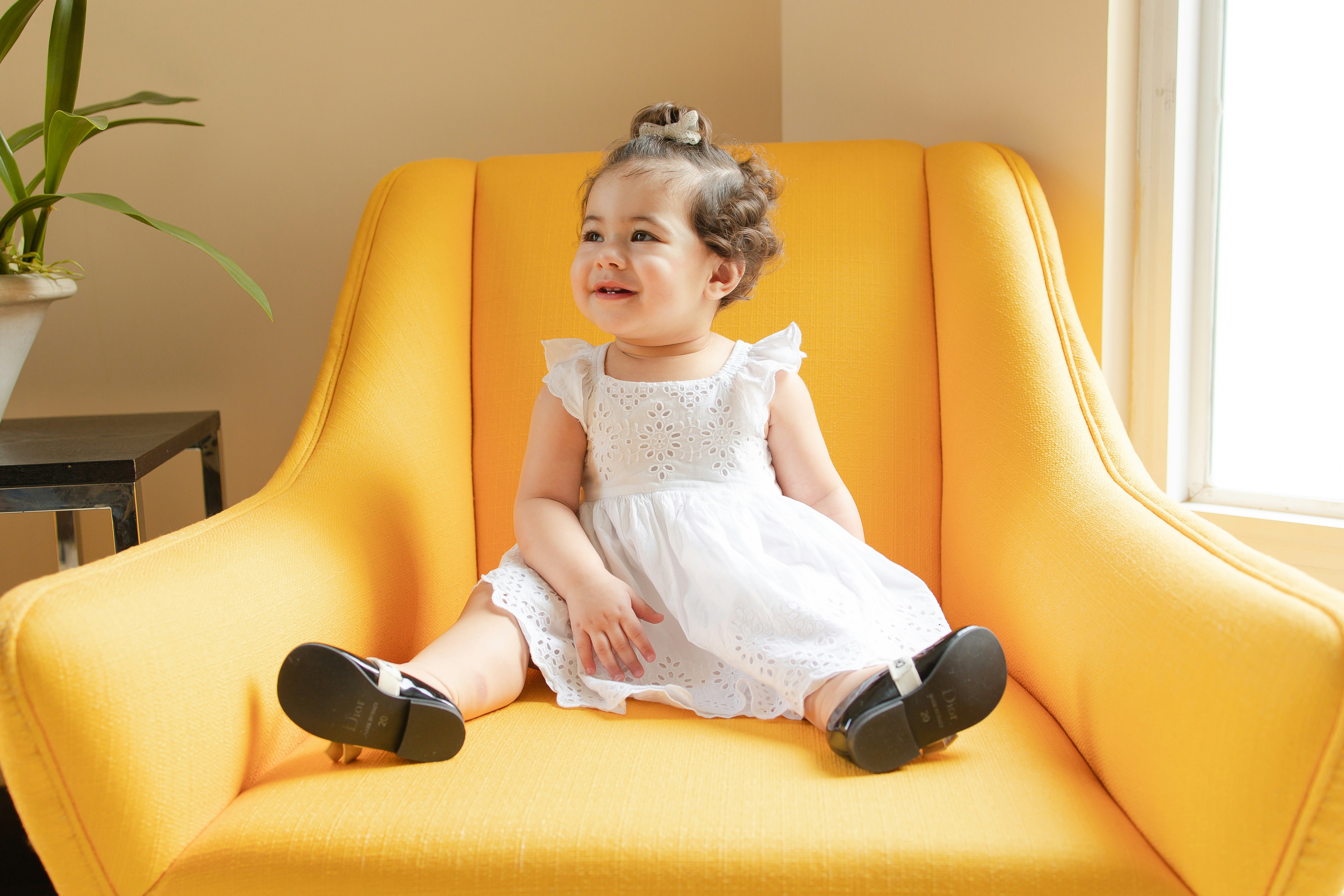 A baby girl is sitting on a yellow sofa, with happy face and smiling