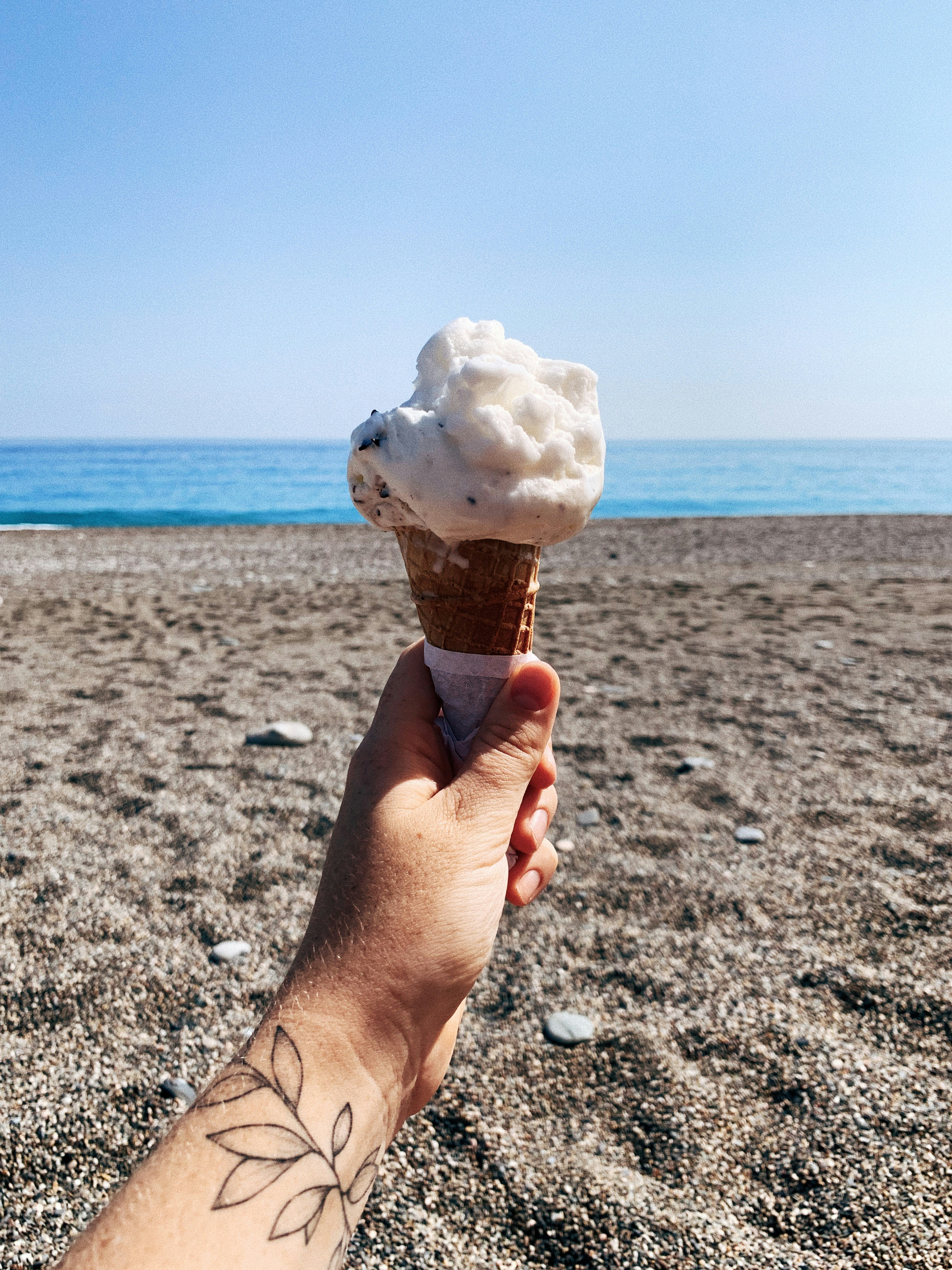 Hand-Held Ice Cream Cone Framed by a Quiet Pebble Beach Seascape