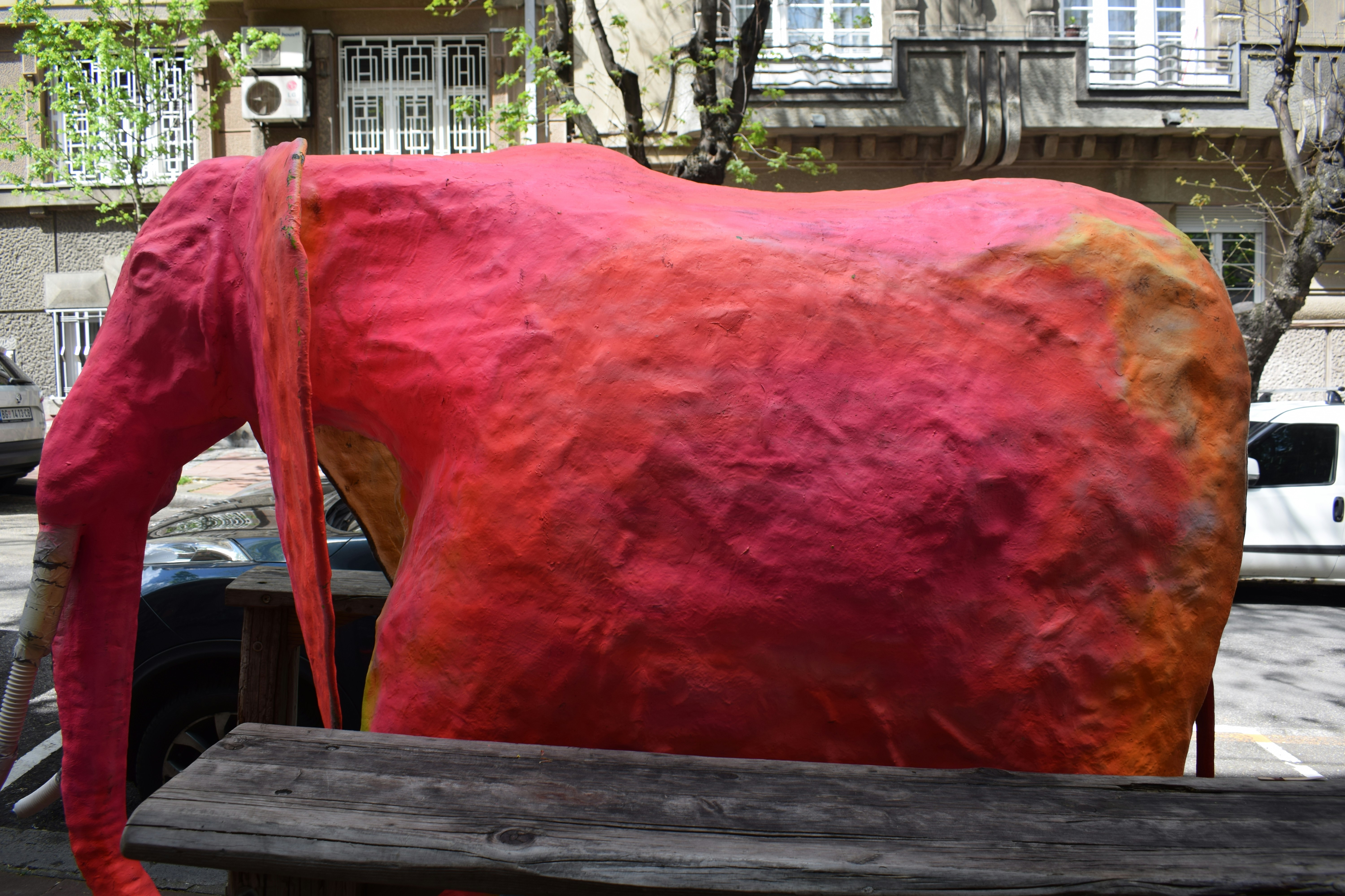 Crimson Elephant Guarding the Street: A Fabric-Textured Giant Beside a Weathered Bench
