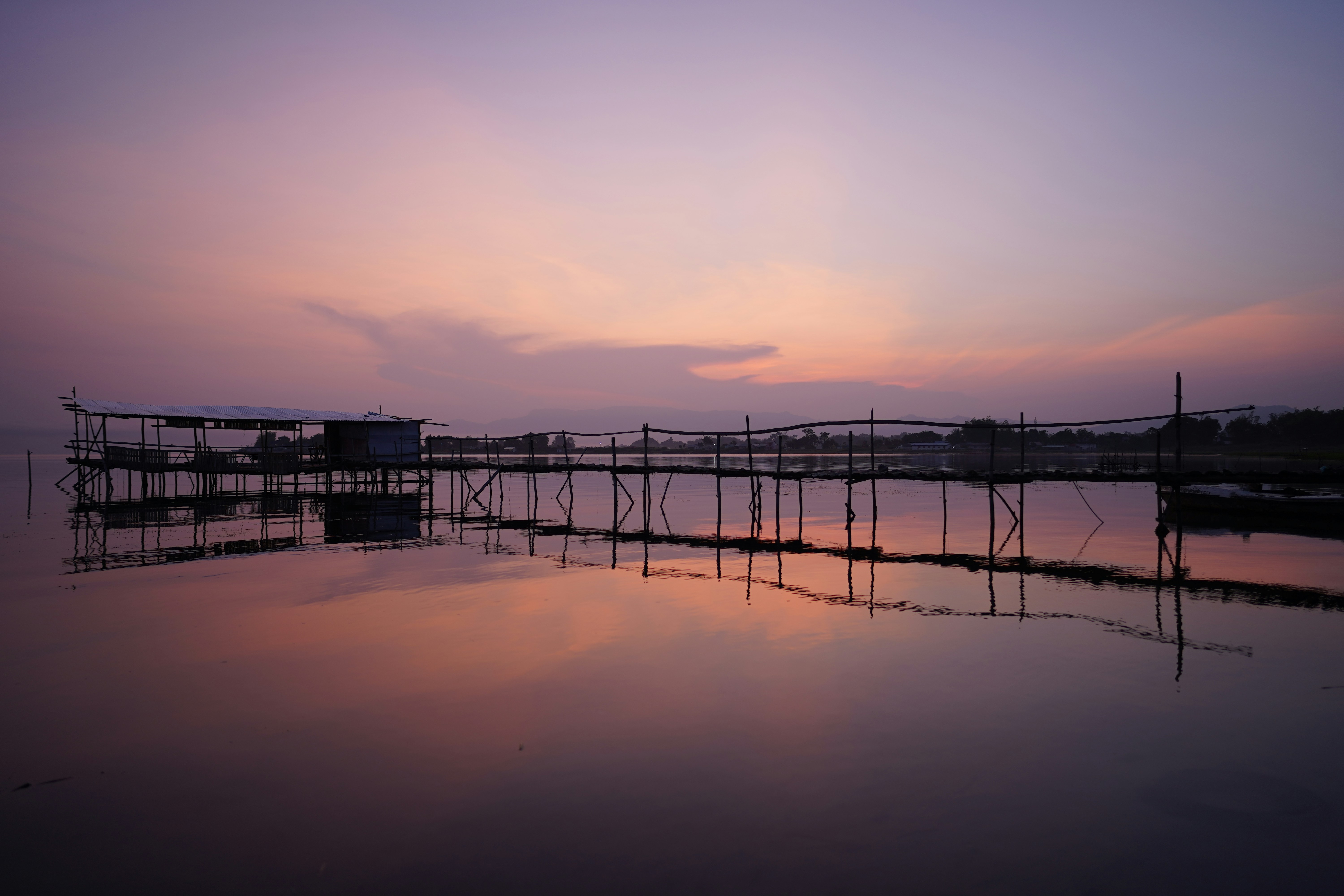 Serene sunset casting pastel hues over a calm sea with silhouetted structures in the distance.