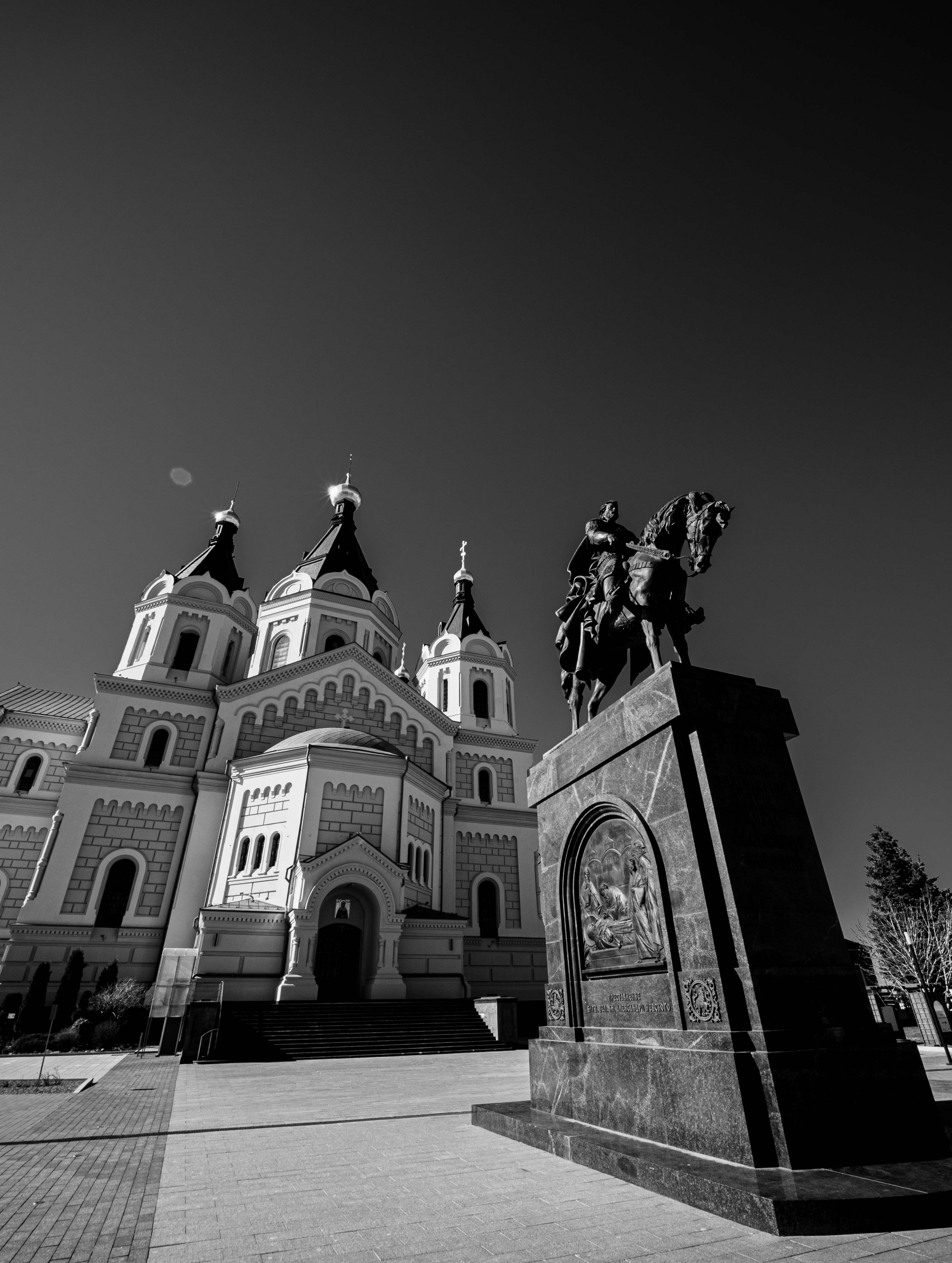 Black and white photo of a grand cathedral with domes beside a horseback statue under a clear sky.
