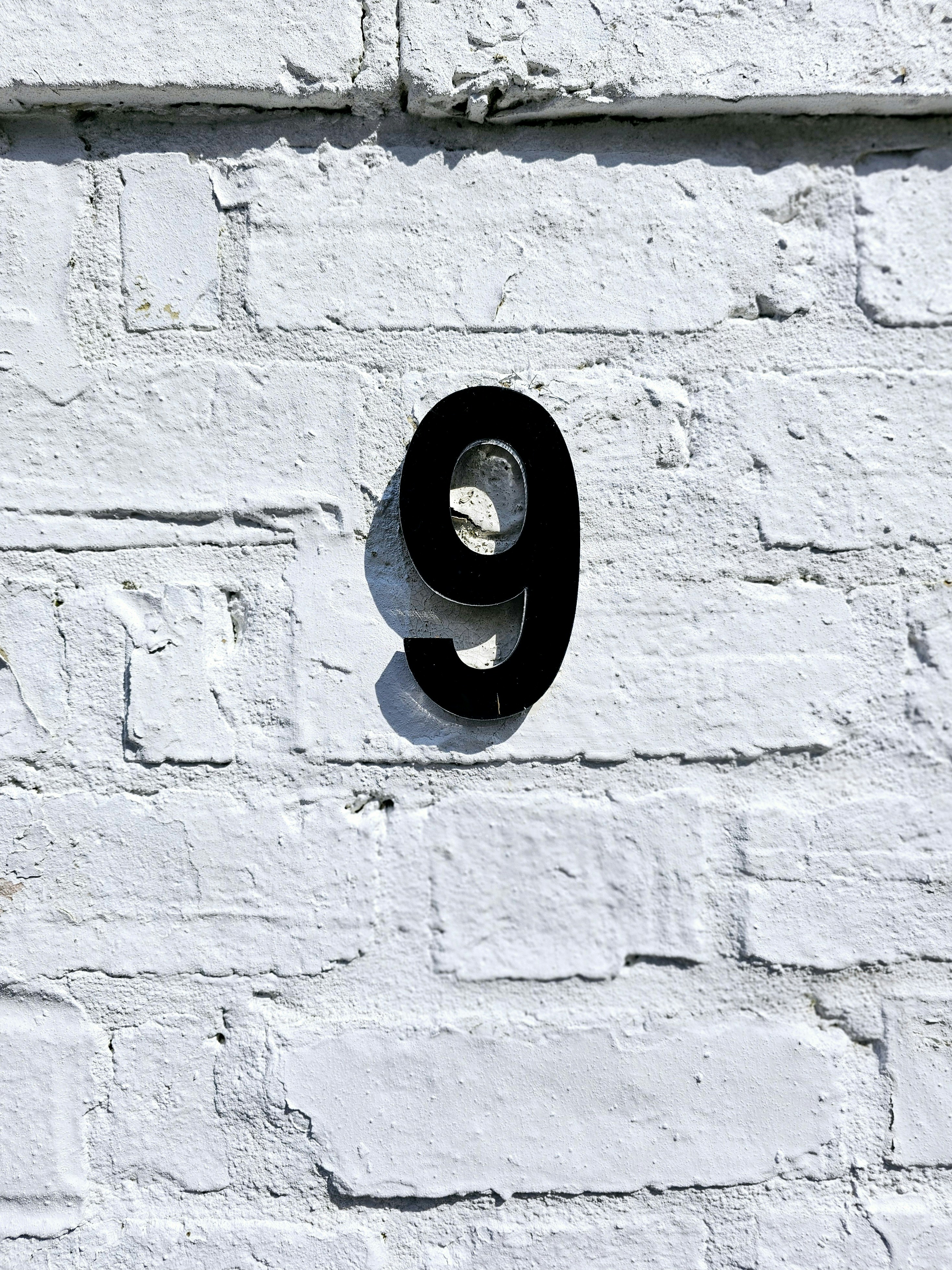 A white brick wall with a black number nine on it photo – Free White ...