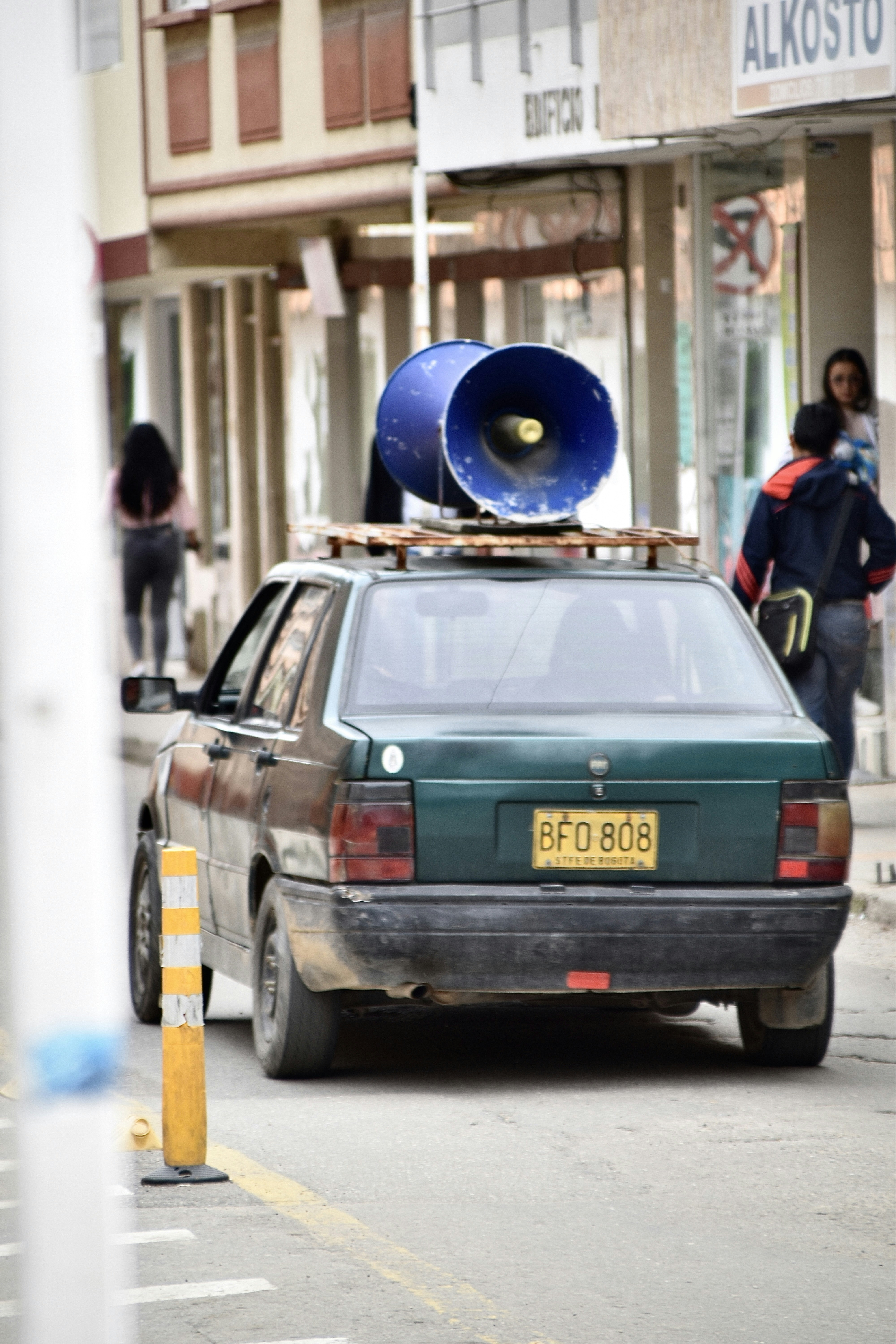 Car equipped with a speaker on its roof, driving through a small town street.