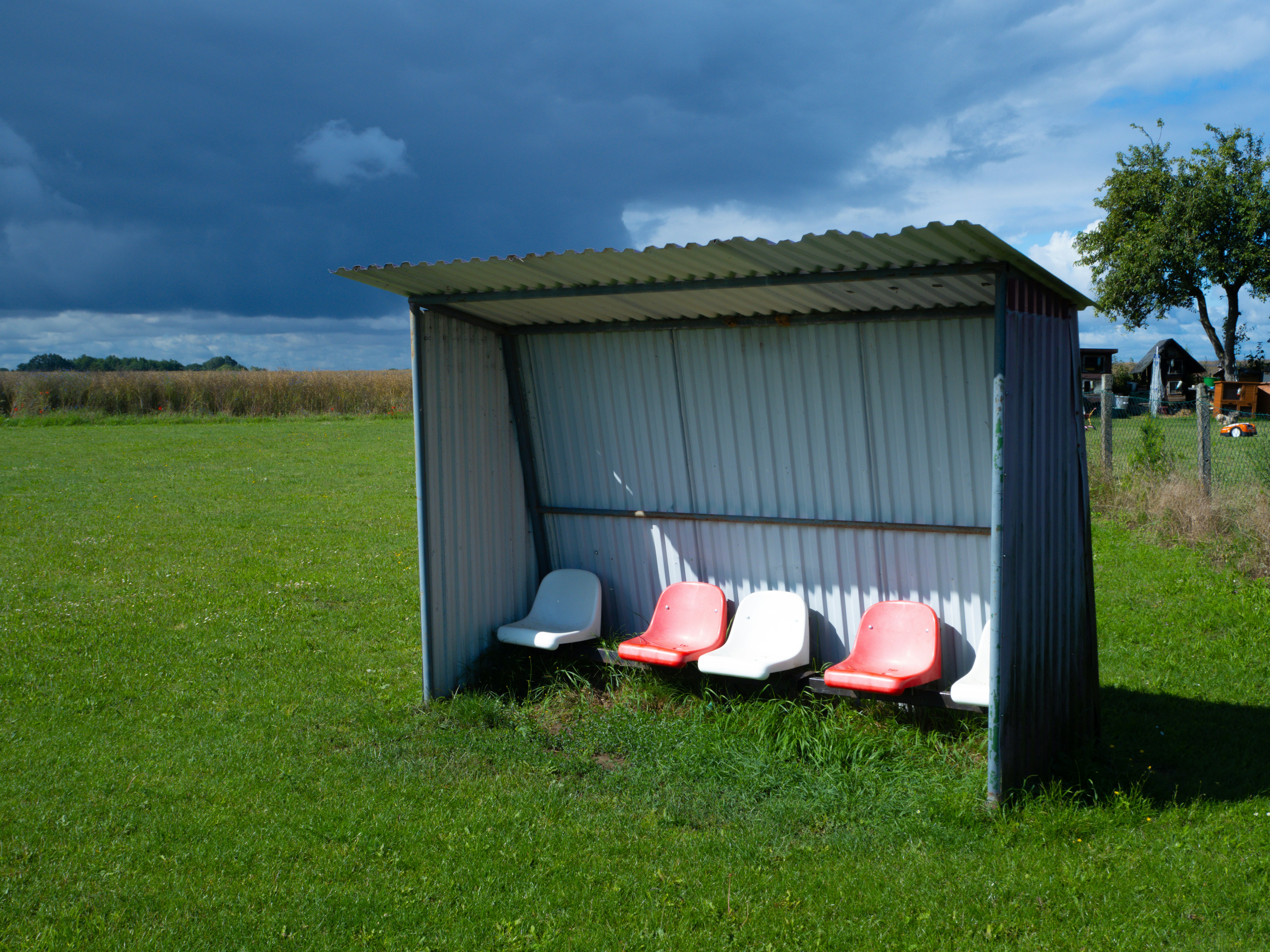 Red-and-White Seats at a Rural Bus Shelter Under a Stormy Sky