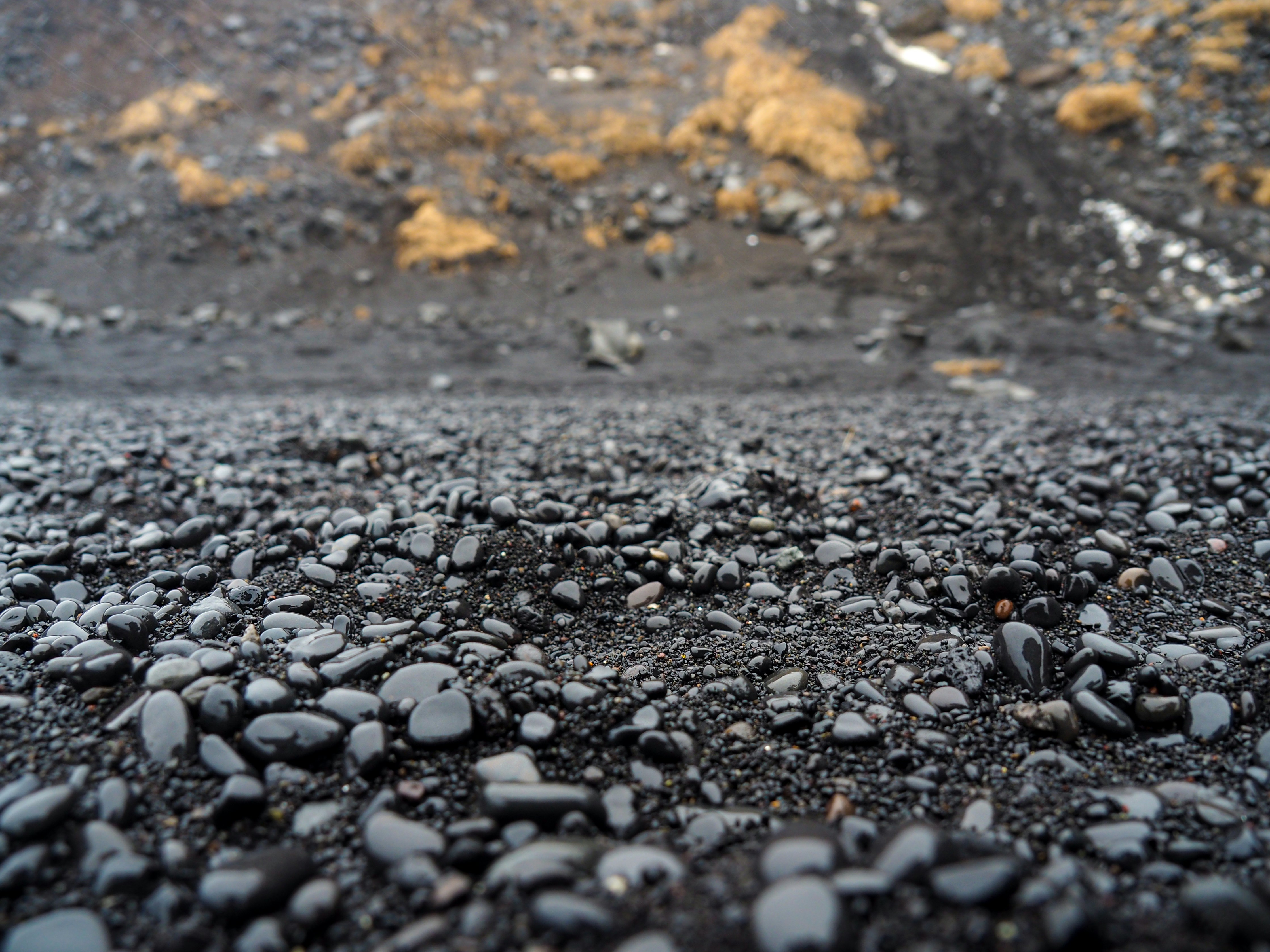 Close-up view of a textured black pebble surface with hints of golden earth in the background.