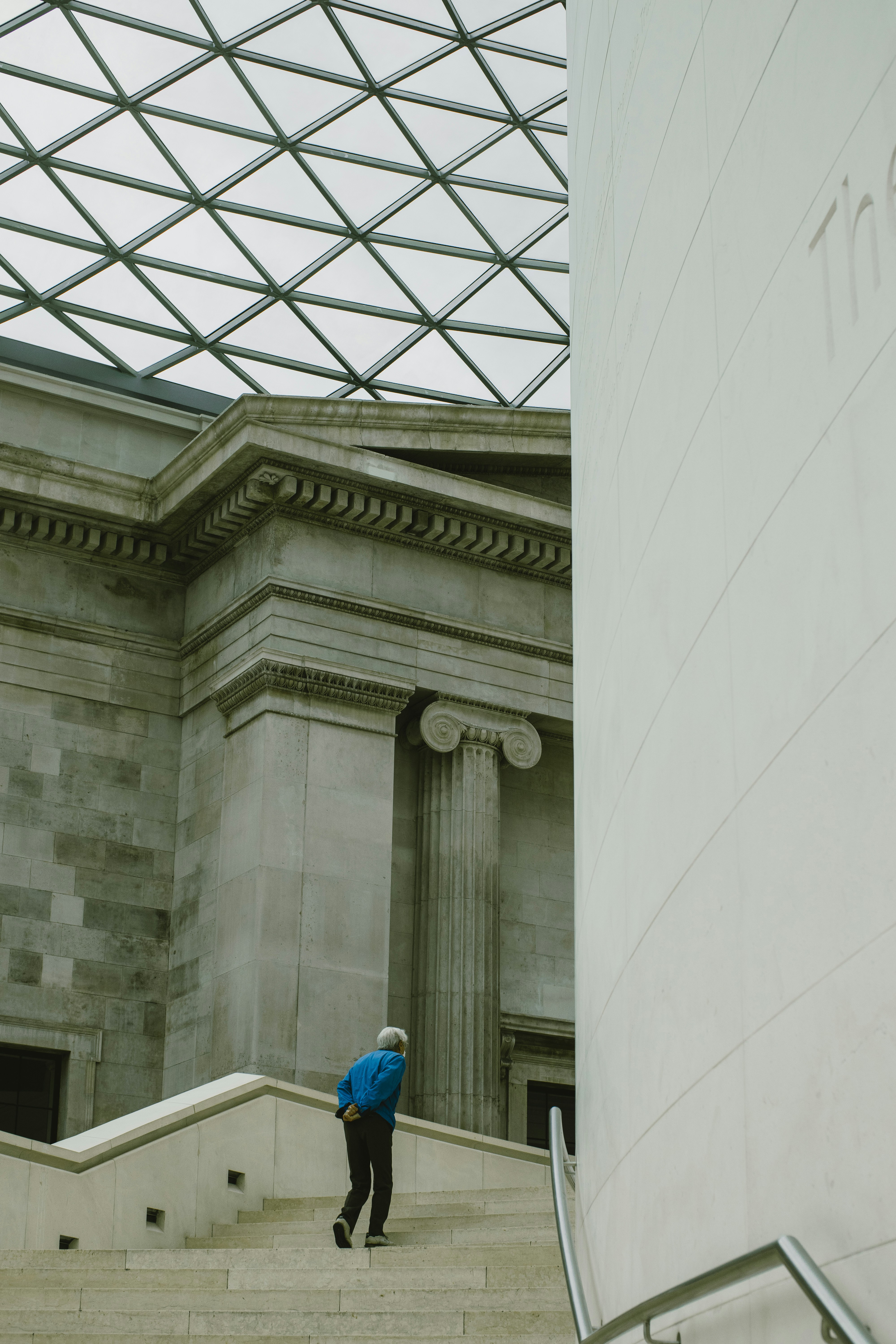 Blue-Clad Figure Ascends Marble Stairs Under a Geometric Glass Skydome