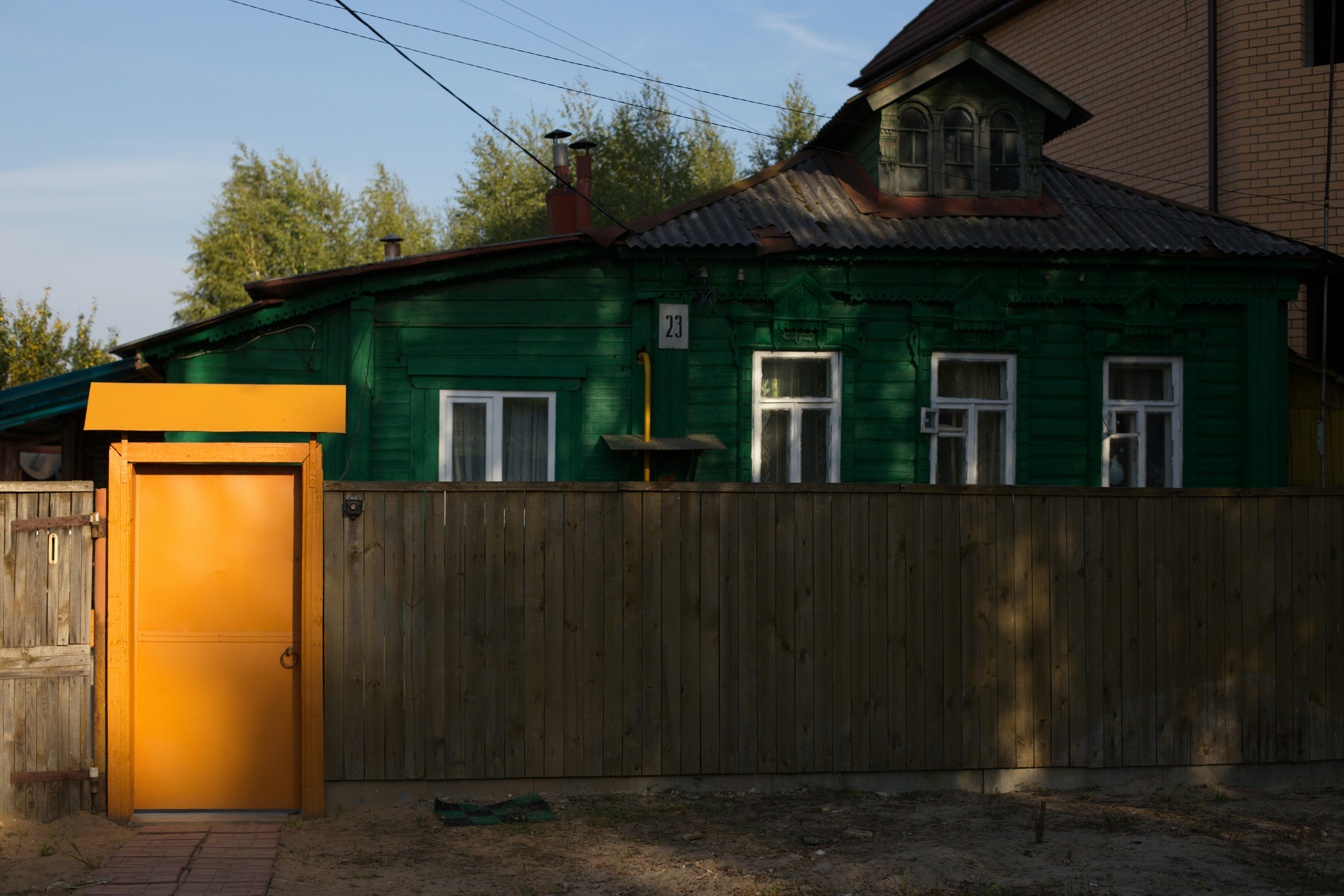 a green house with a yellow door and a wooden fence