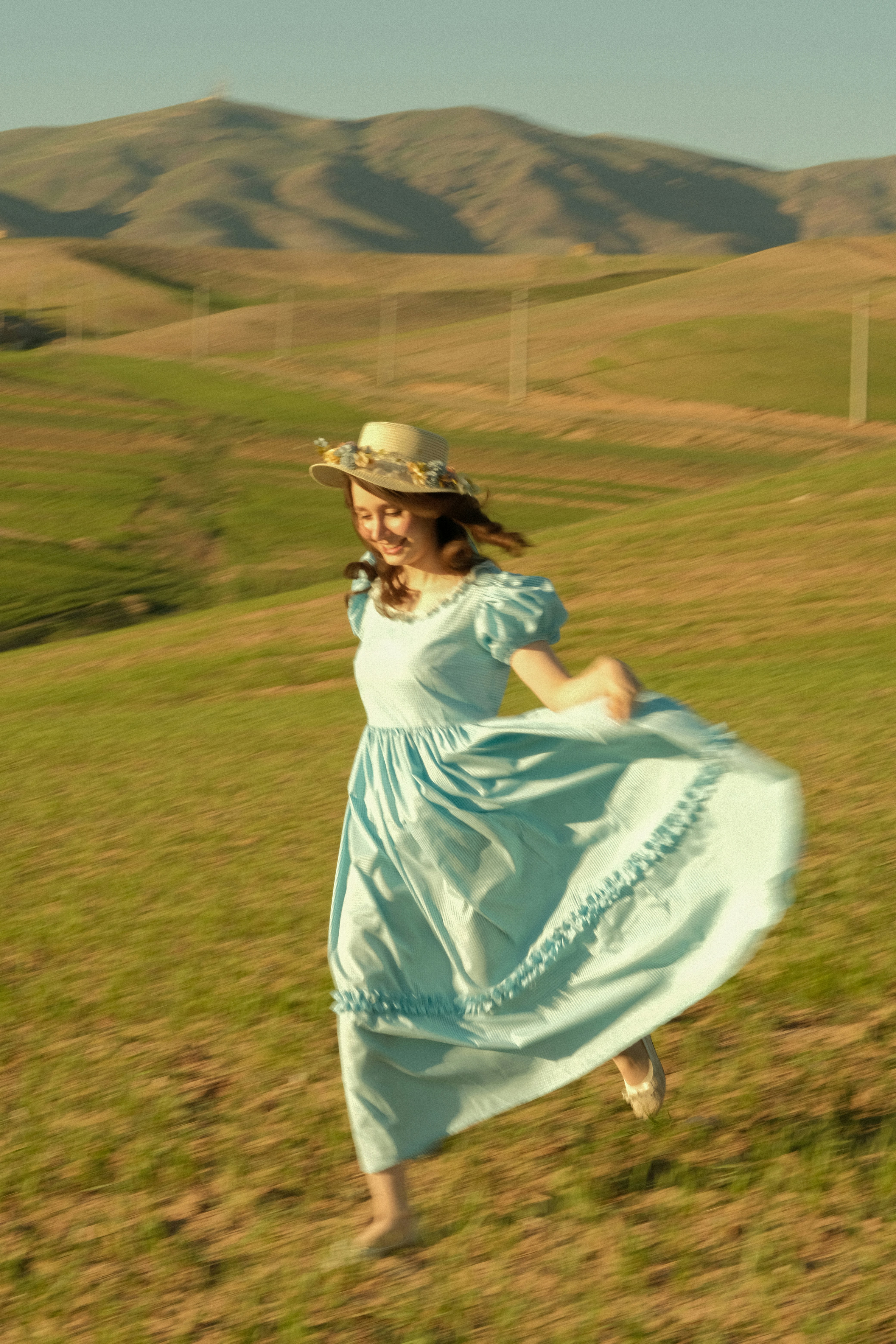 a woman in a dress and hat running through a field