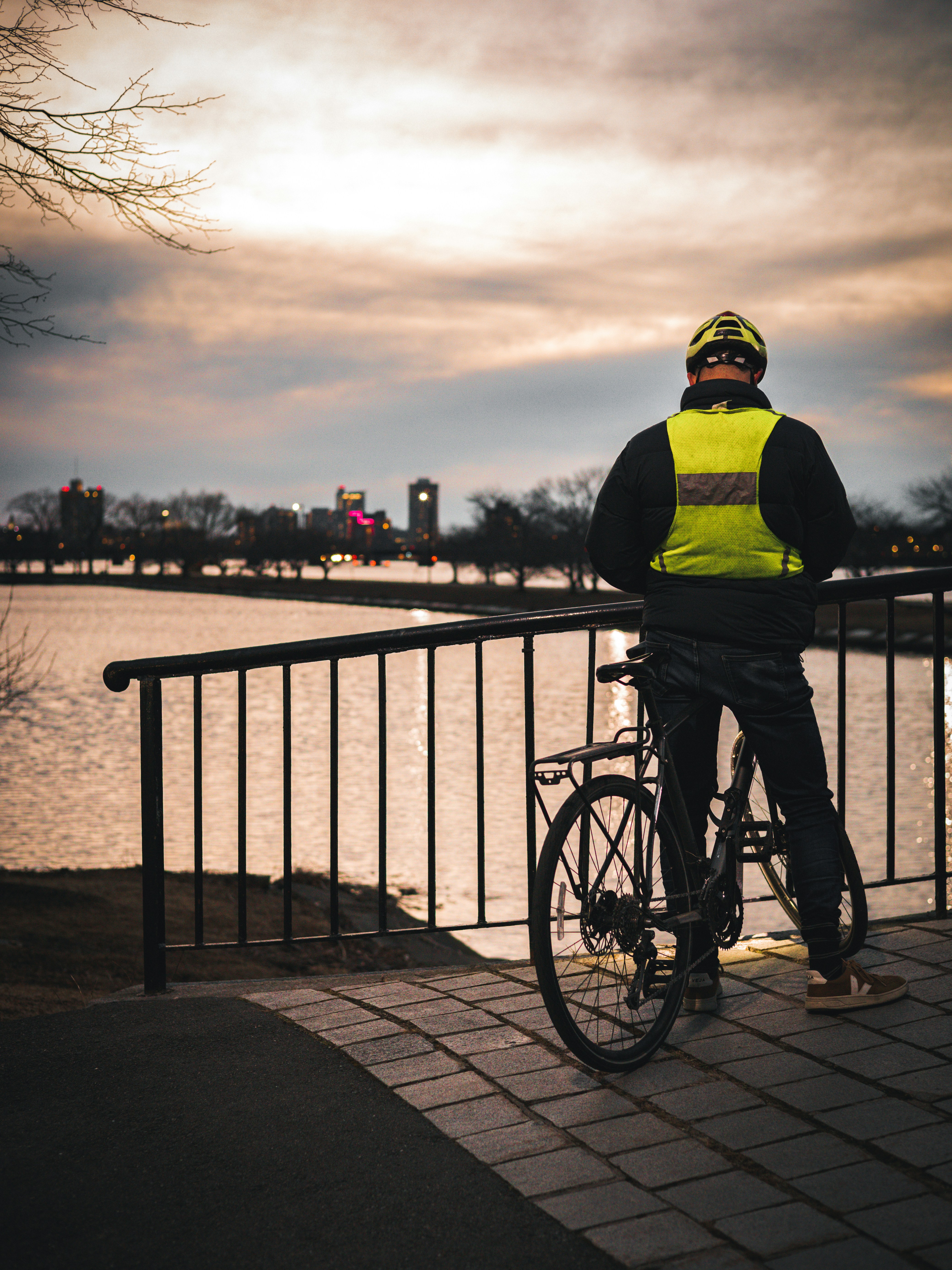 Twilight by the River: A Neon-Vest Cyclist Gazes Toward the Distant City