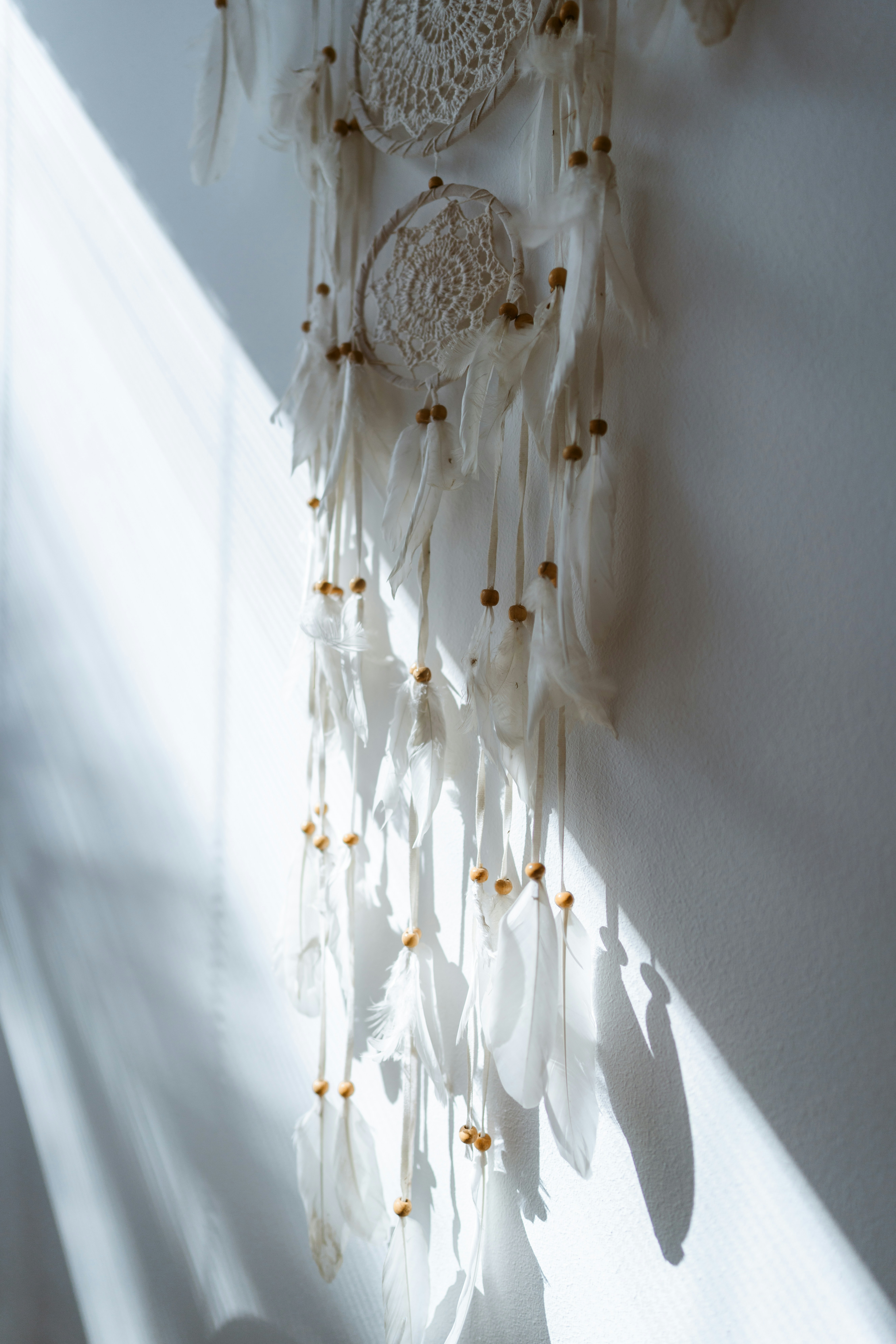 Sunlit Dreamcatcher: Feathers and Shadows on a White Wall
