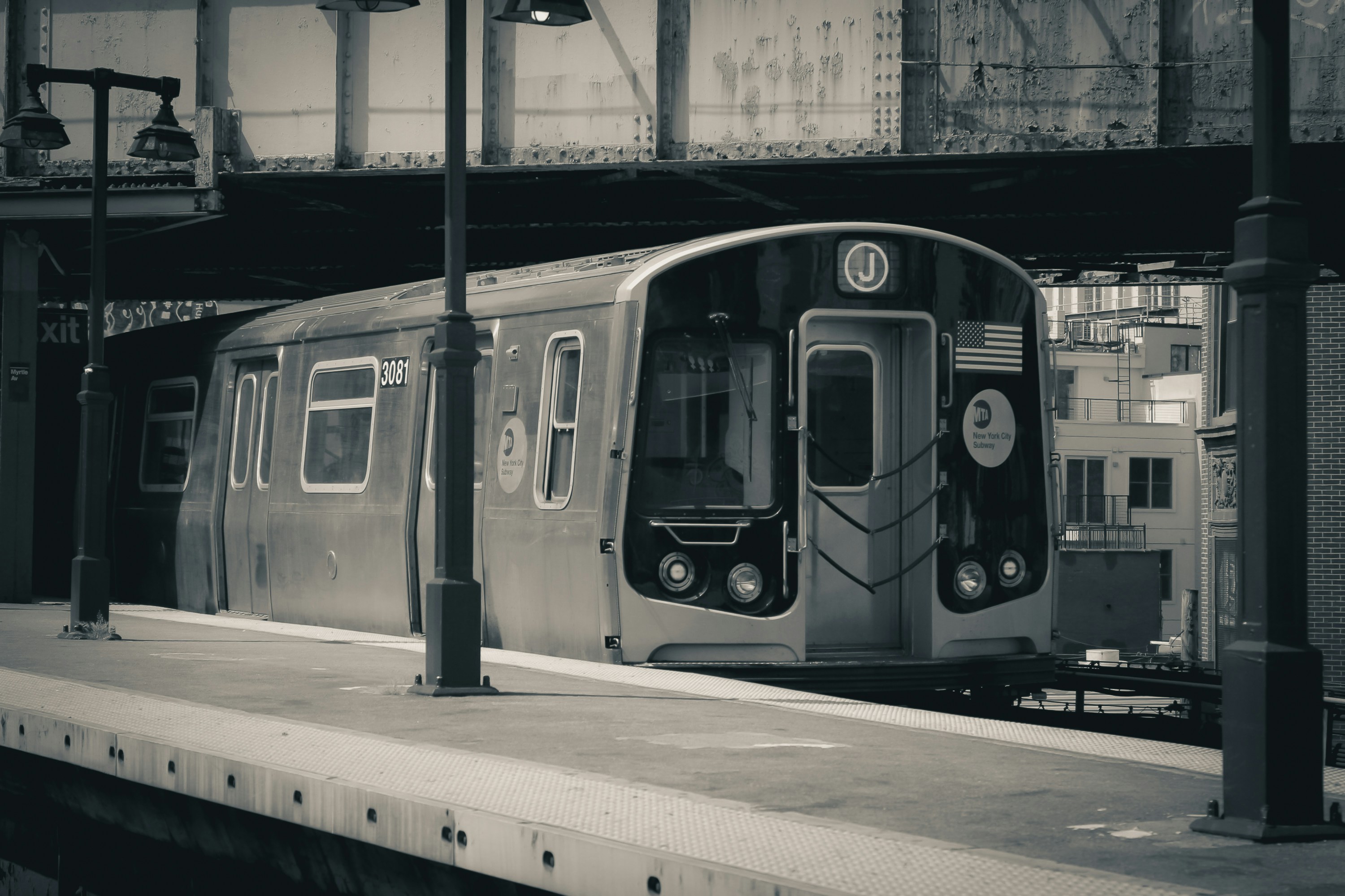 Subway train poised at the platform, surrounded by urban architecture in a black-and-white setting.