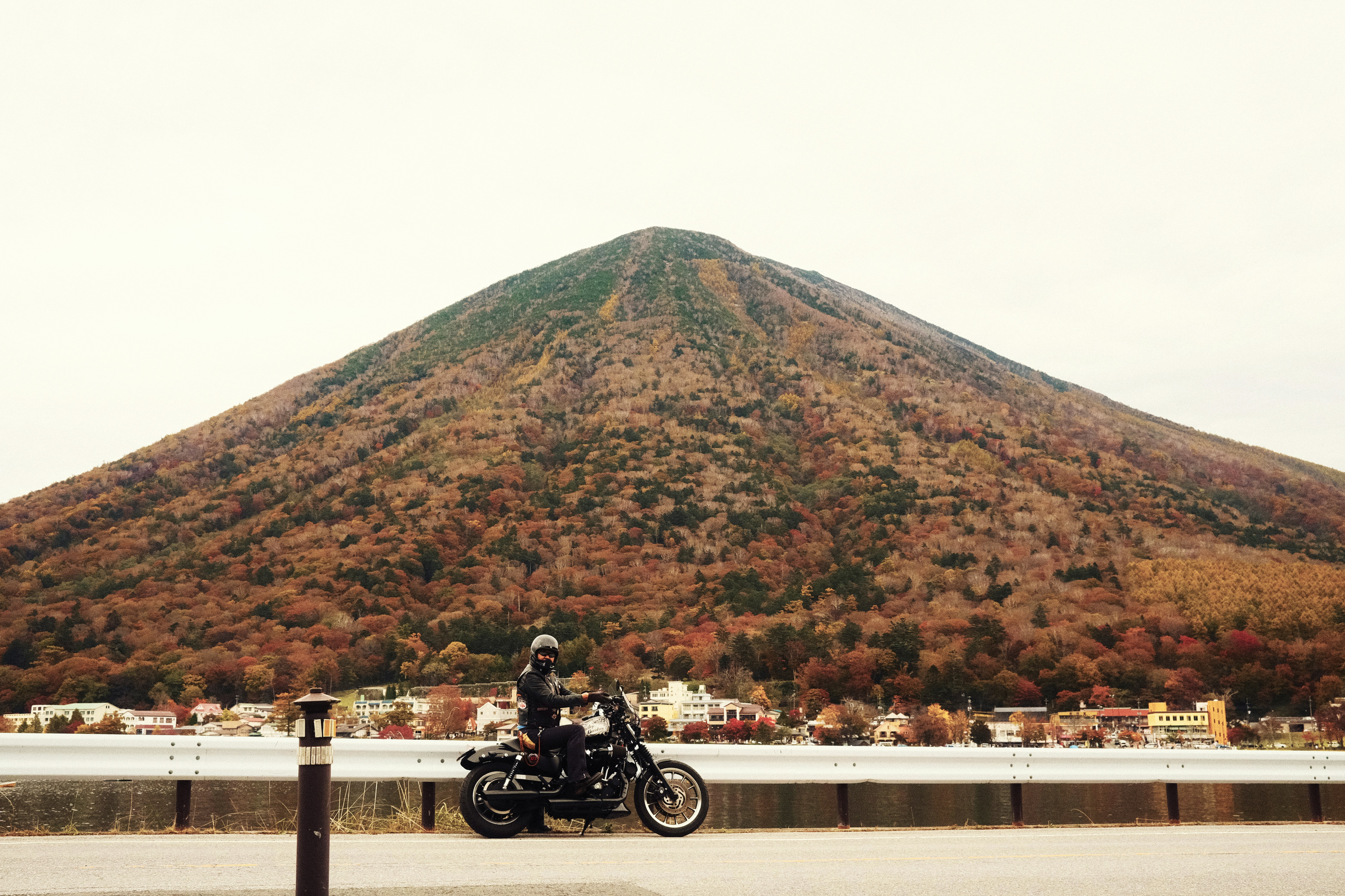 Autumn Roadfront: Lone Motorcyclist Beneath a Crimson-Hued Mountain