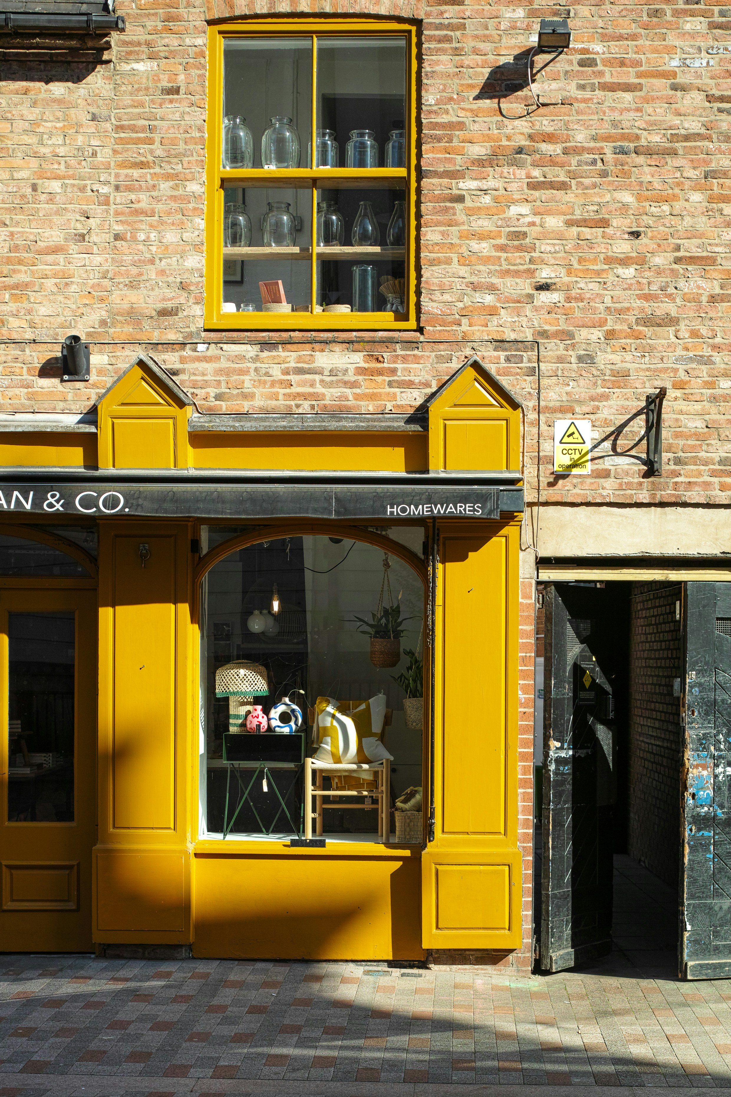 Sunlit yellow storefront on a brick building with a glass window display of homewares.