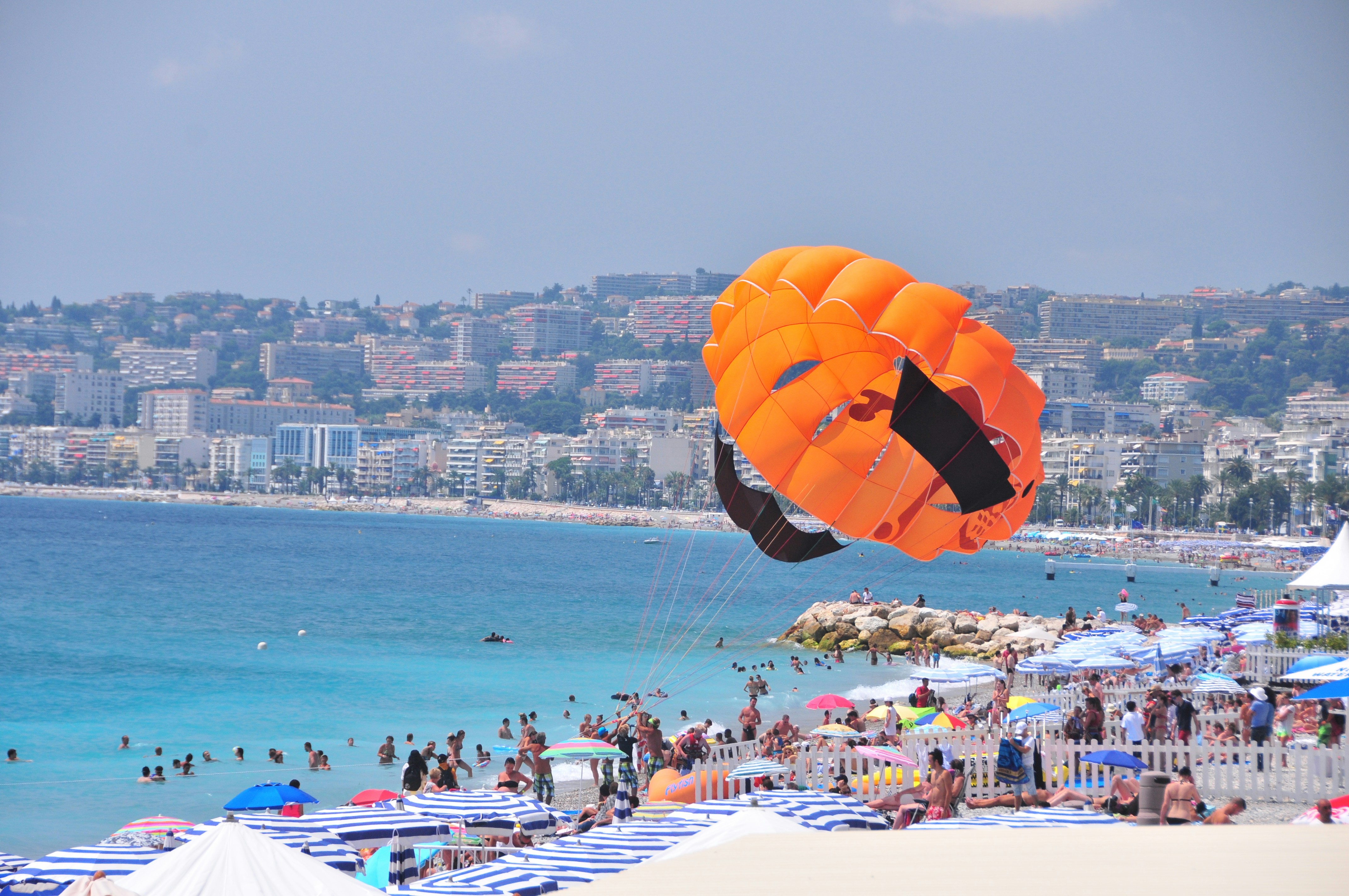 Bright orange parasail over a sunlit Mediterranean beach scene