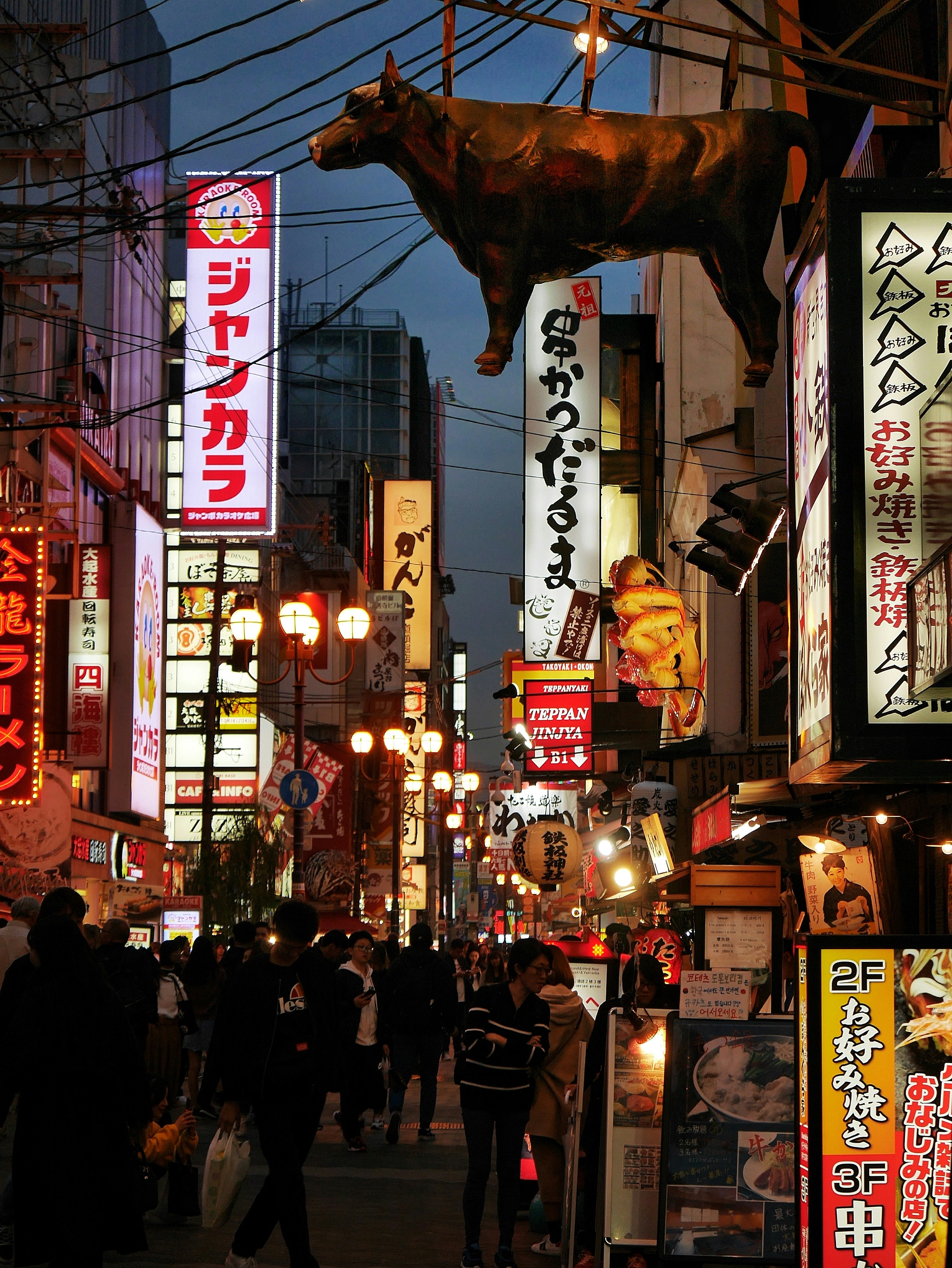 Kobe by night | a busy city street at night with a statue of a cow