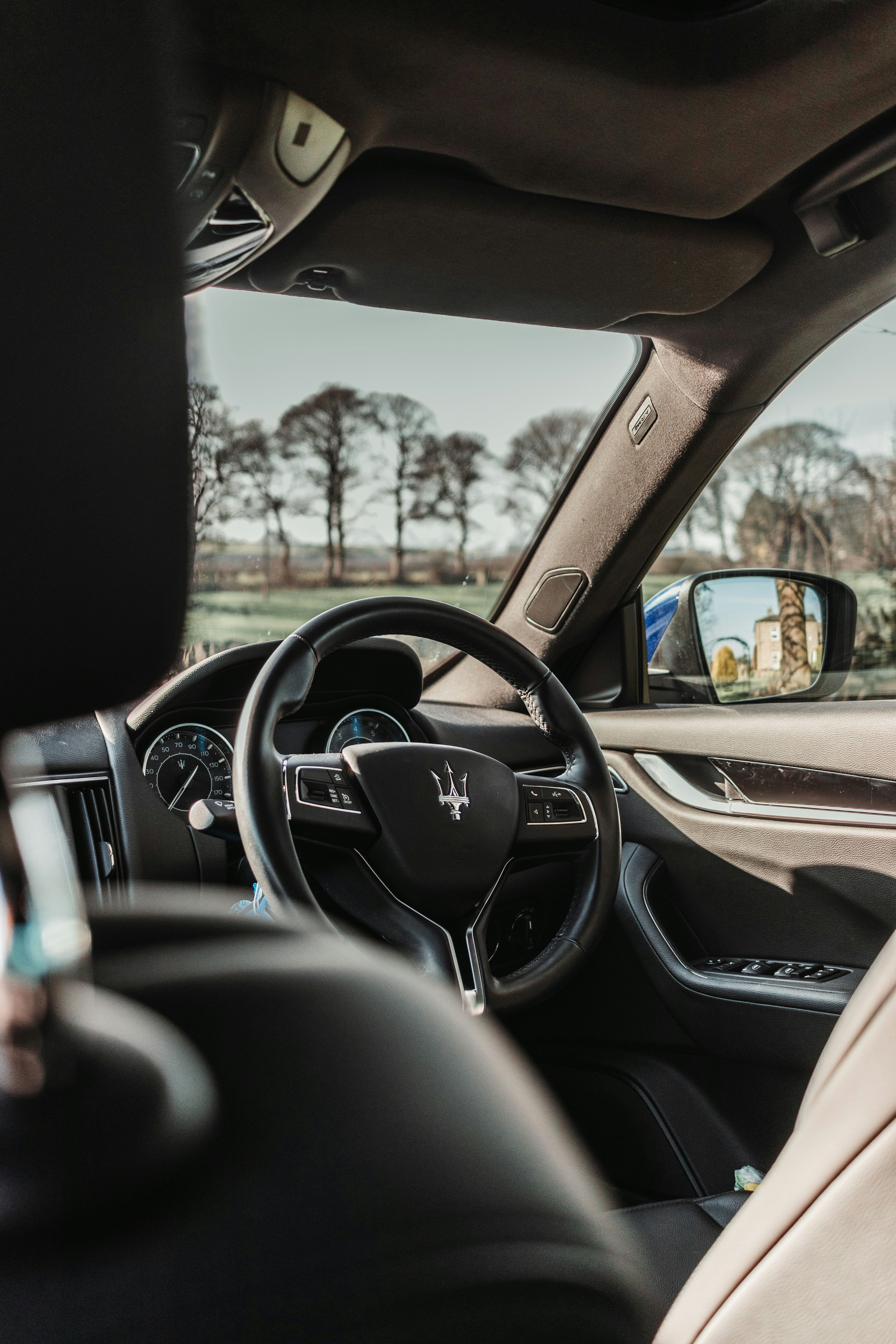 Trident at the Helm: A Maserati Cockpit Framed by a Quiet Road View