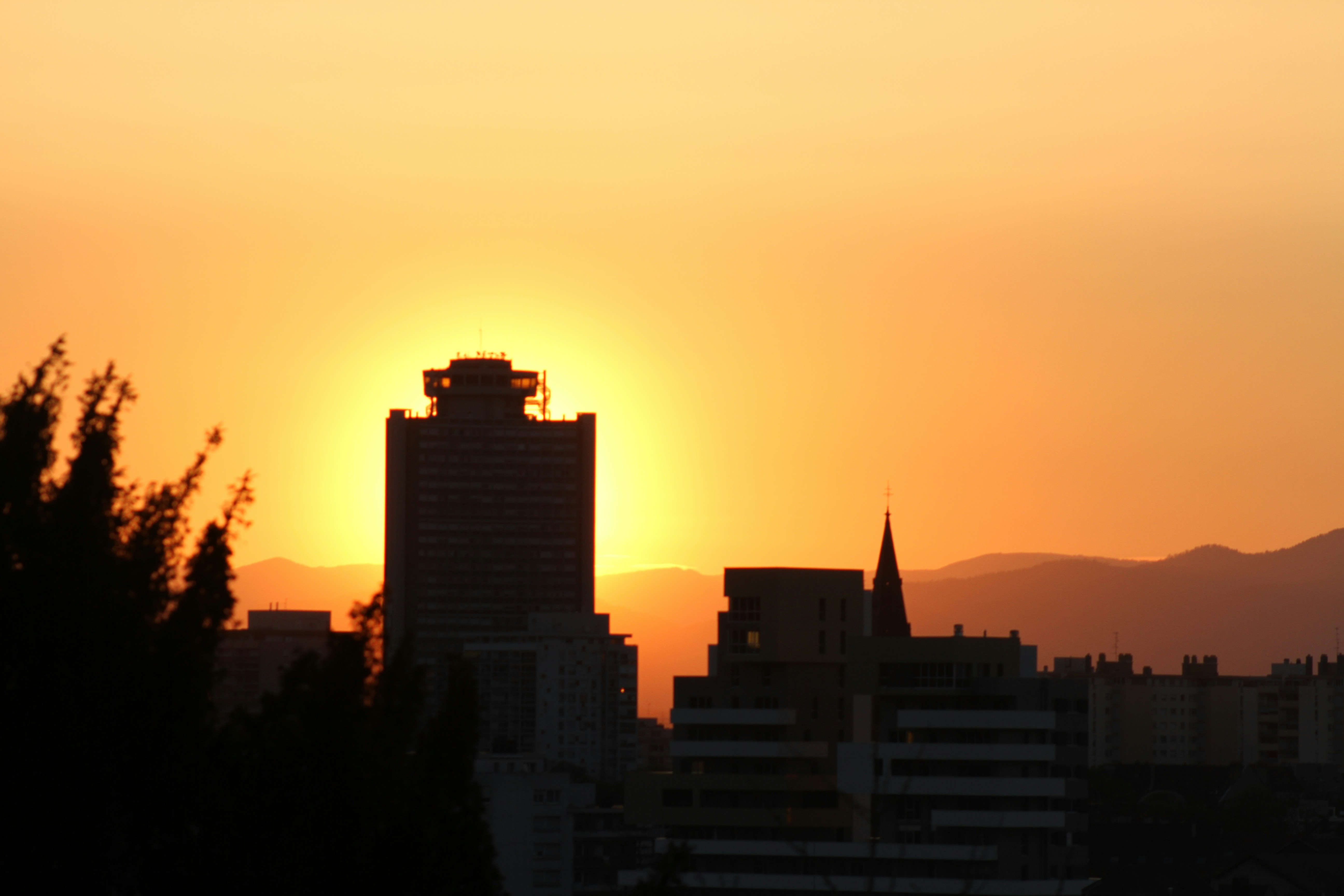 Silhouetted cityscape of Mulhouse against a vibrant sunset, with the Europe Tower prominently outlined.