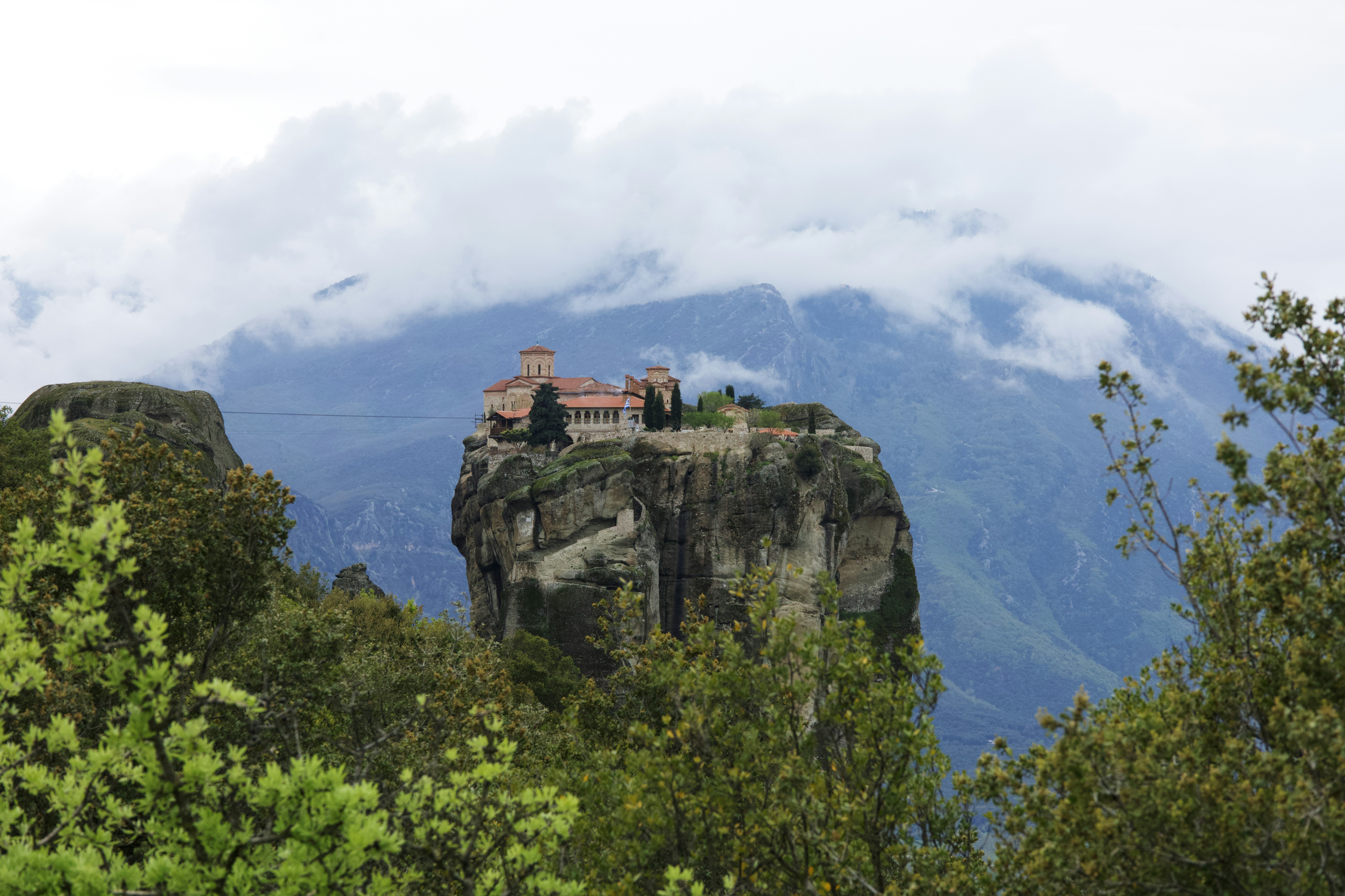 Ancient monastery atop a rocky cliff with mist-covered mountains in the background.