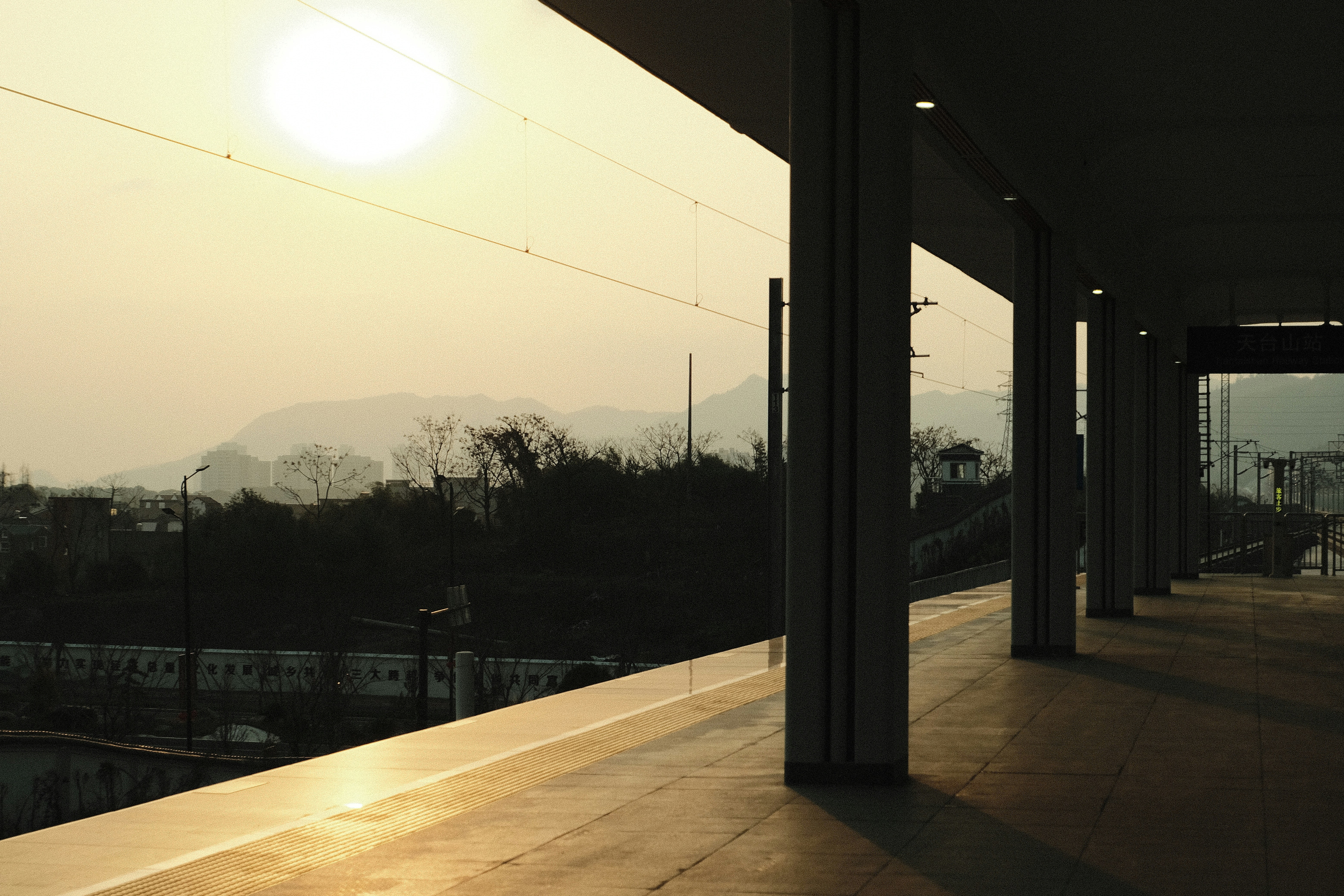 Sunrise over a deserted train platform with silhouetted columns and distant hills.