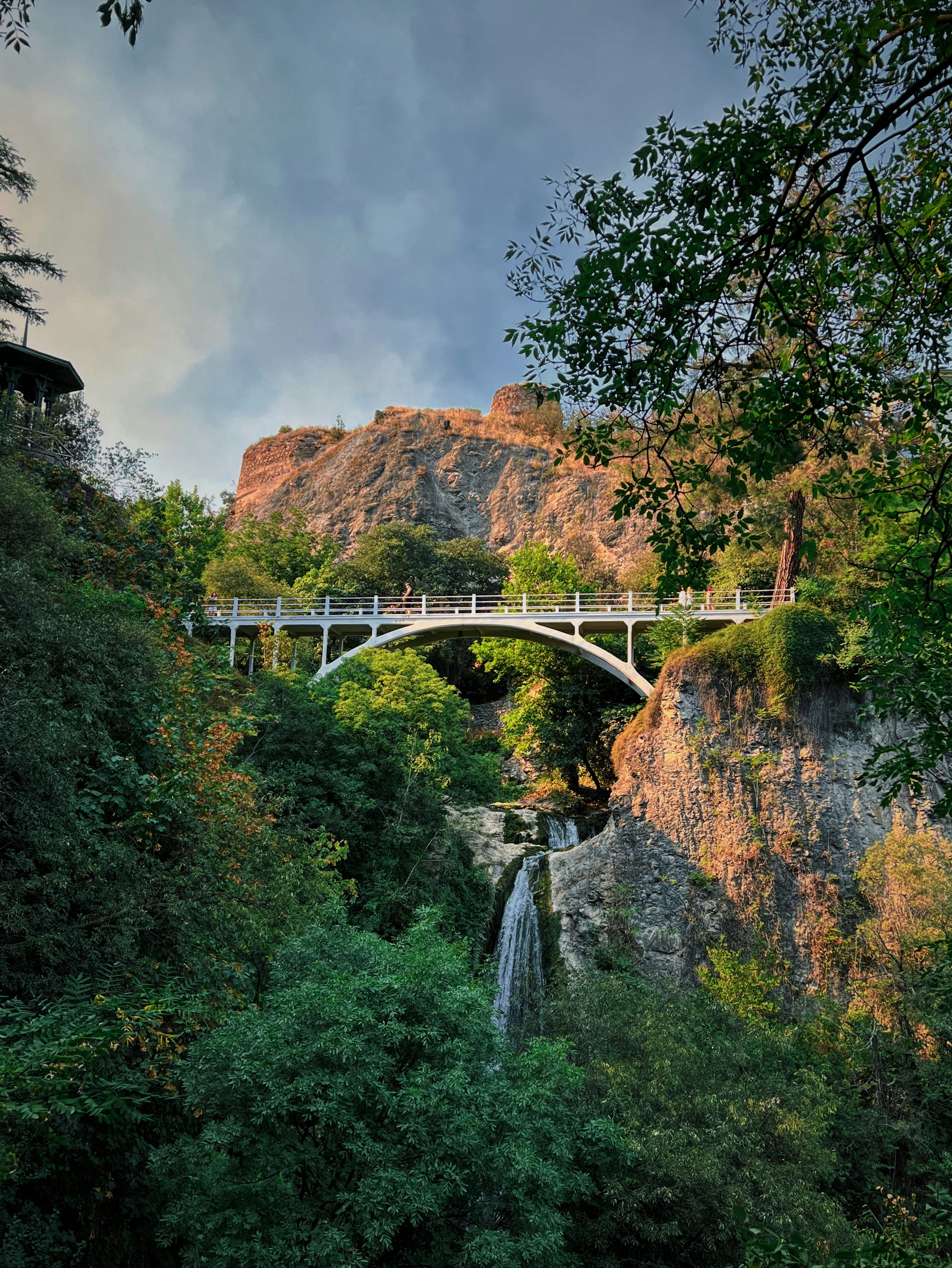 Sunlit Stone Arch Over Verdant Gorge with Cascading Waterfall