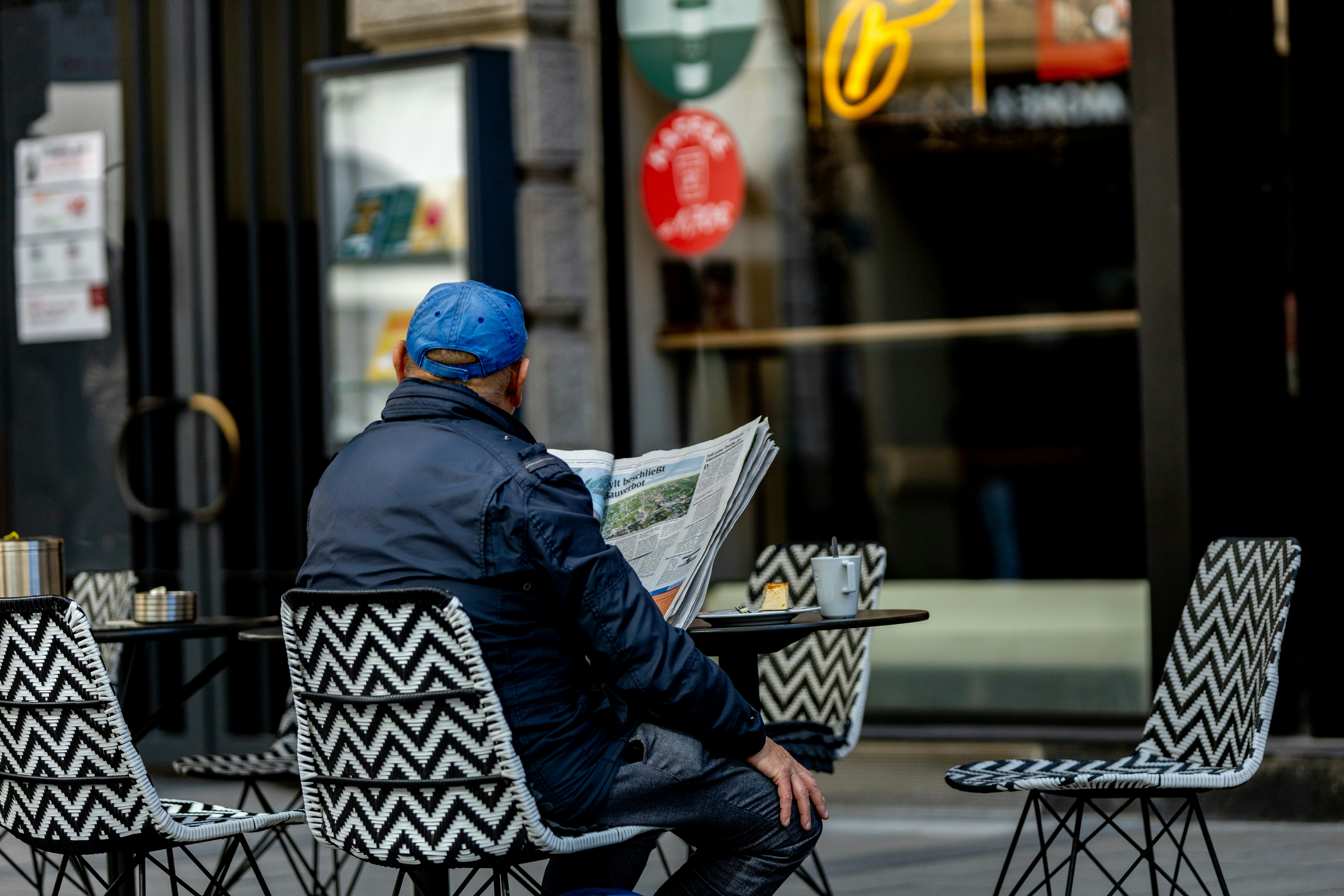 A Quiet Read at the Zigzag Café: Man in a Blue Cap Absorbed in a Newspaper