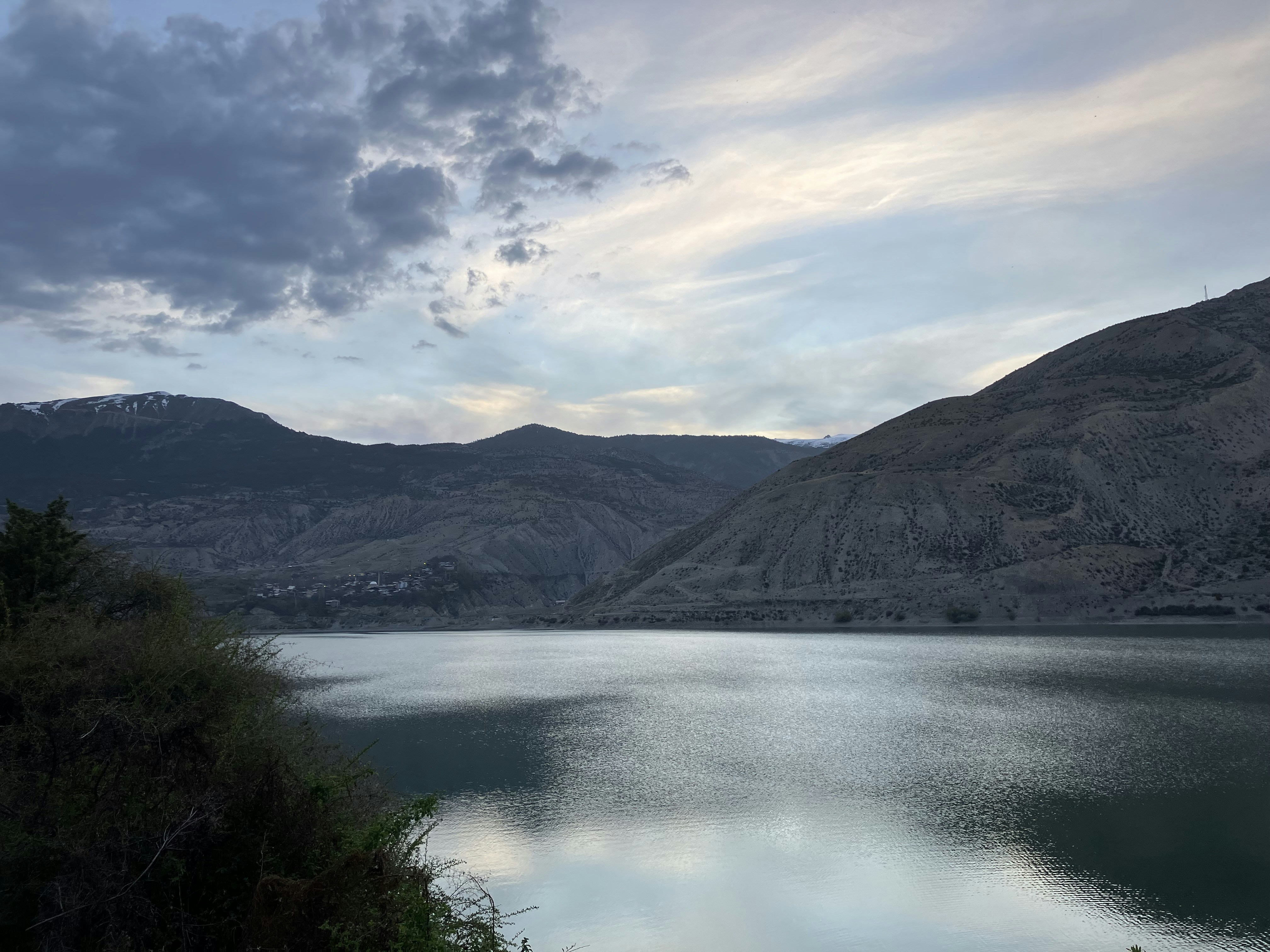 Calm lake reflecting a cloudy sky with silhouetted mountains at dusk.