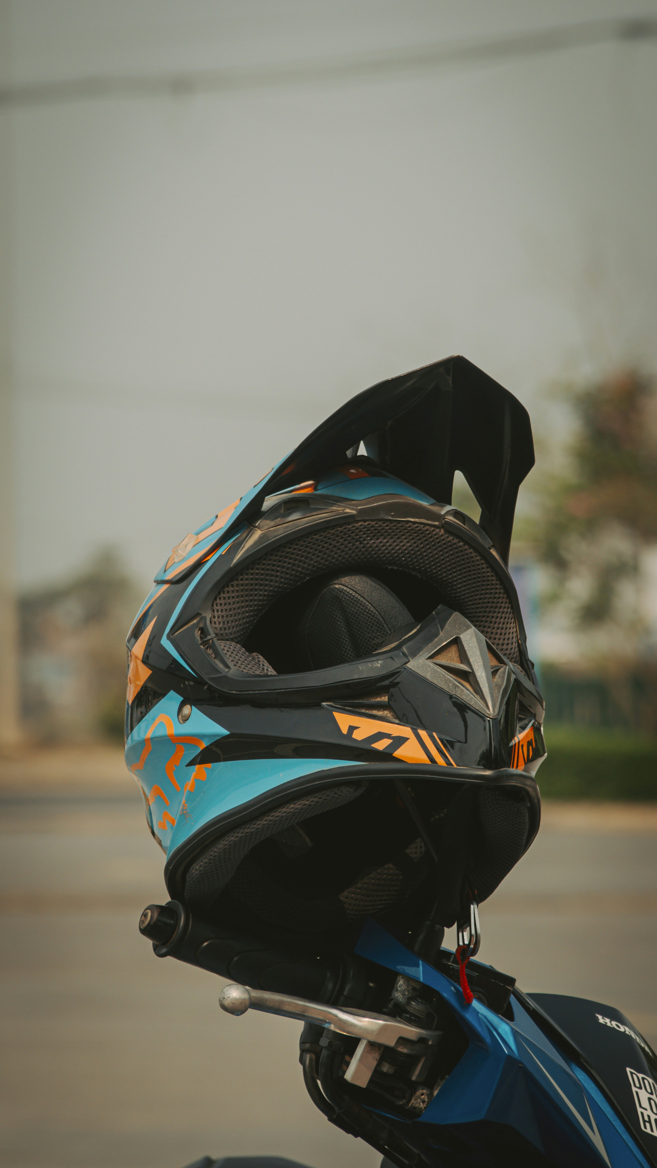 Vibrant blue-orange motocross helmet perched on a blue bike with a softly blurred urban background.