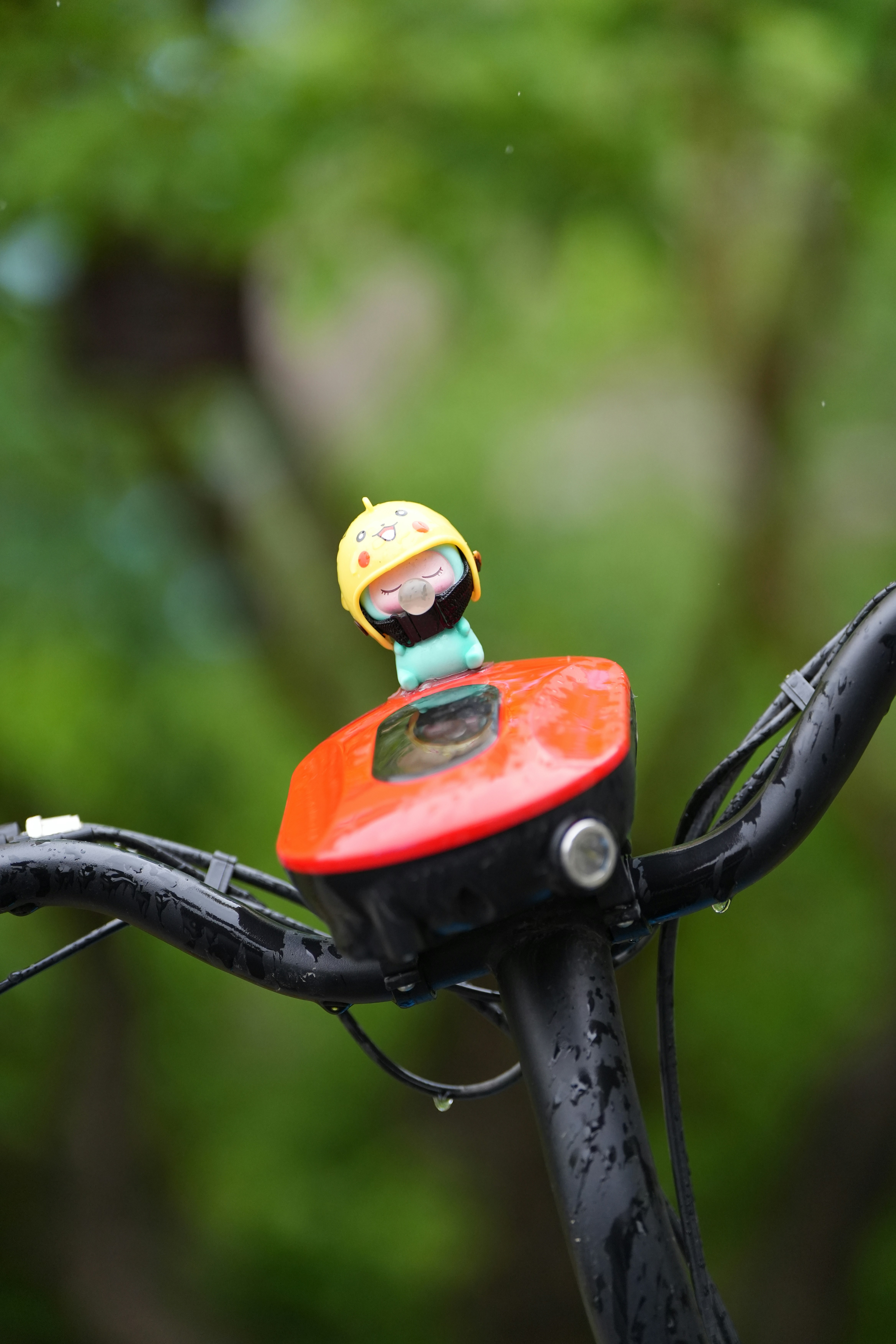 Tiny helmeted figurine perched on a red bike console amid a lush green blur