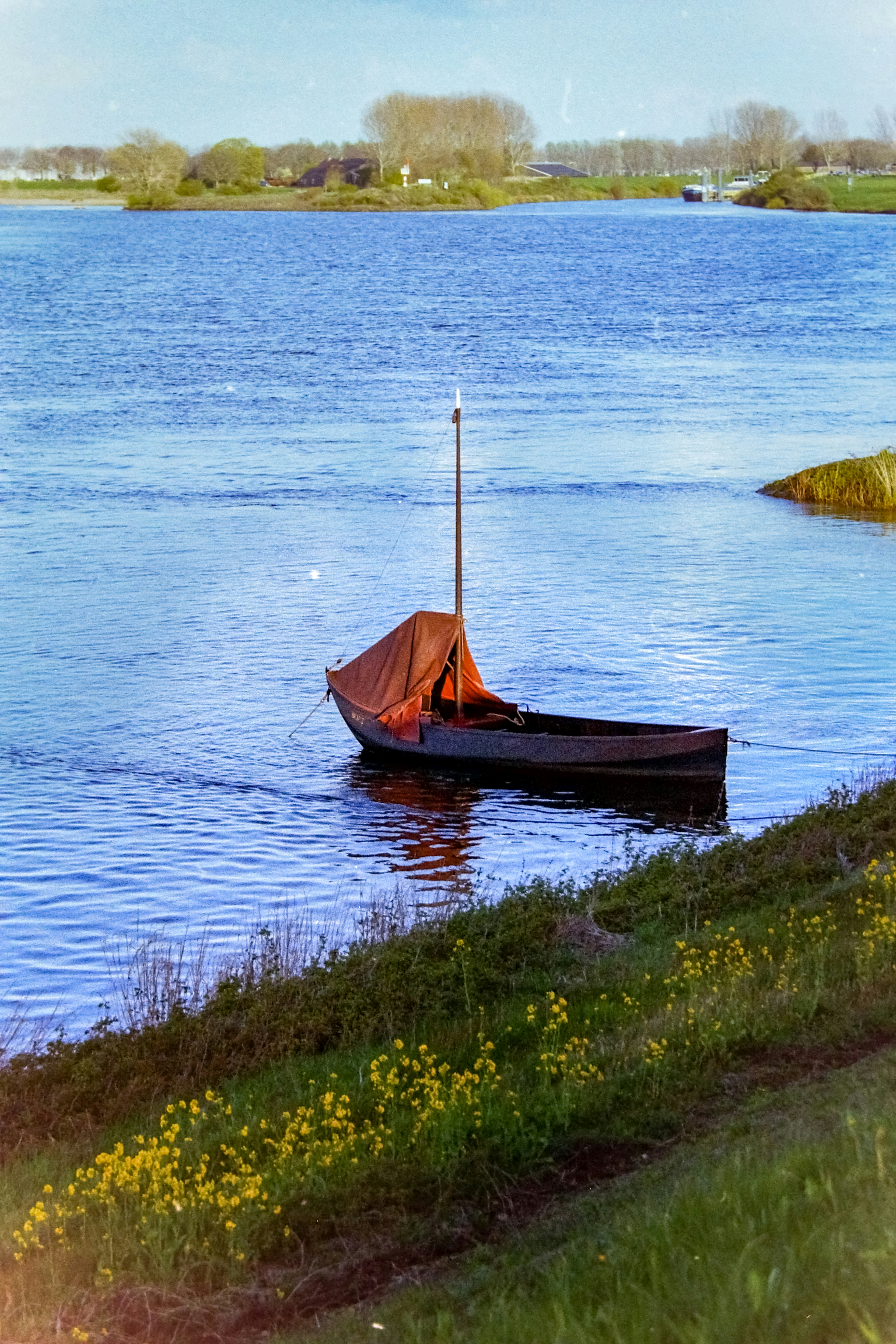 Rust-Colored Sailboat Quietly Anchored Along a Riverside Morning