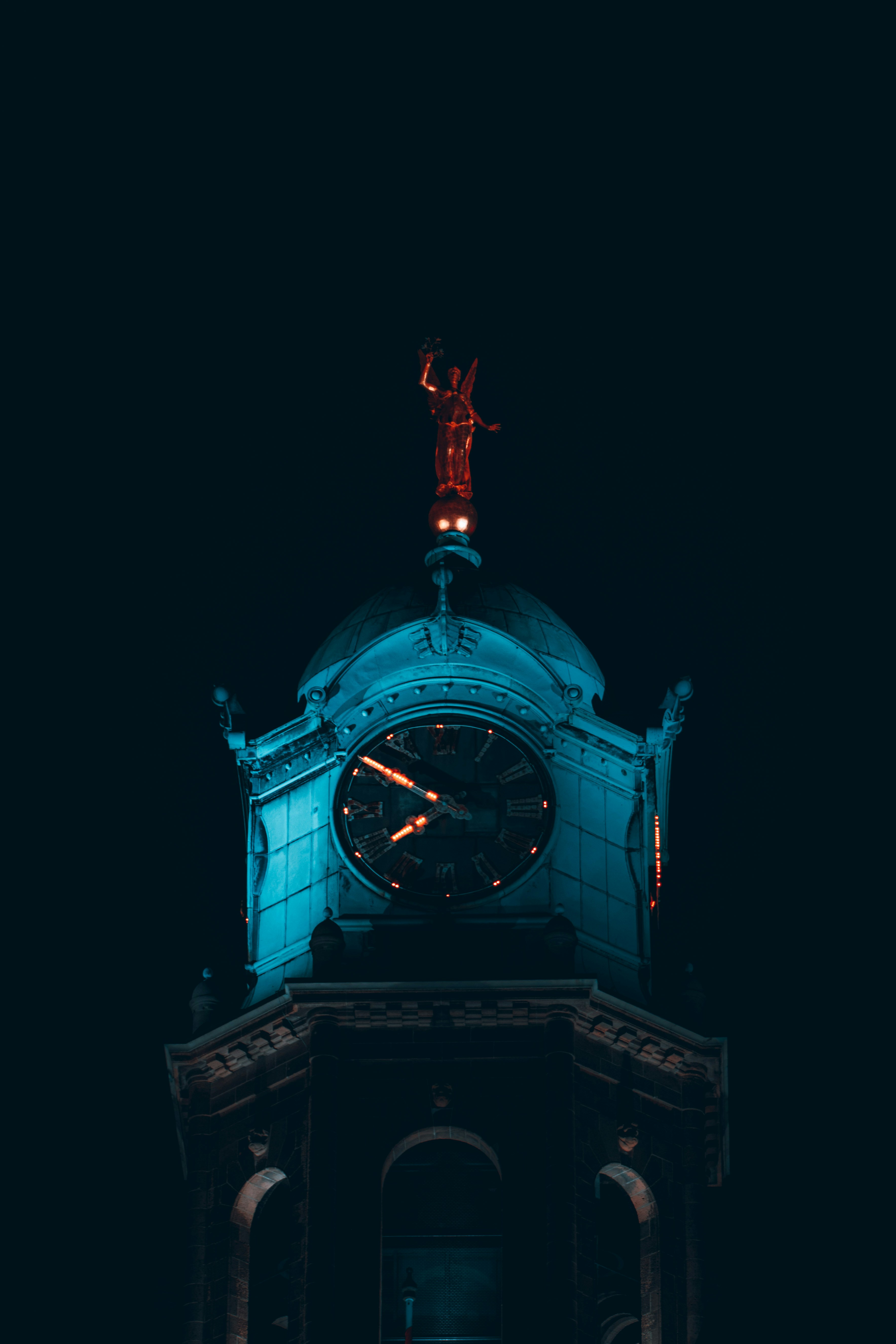 A clock tower lit up at night with a statue on top photo – Free ...