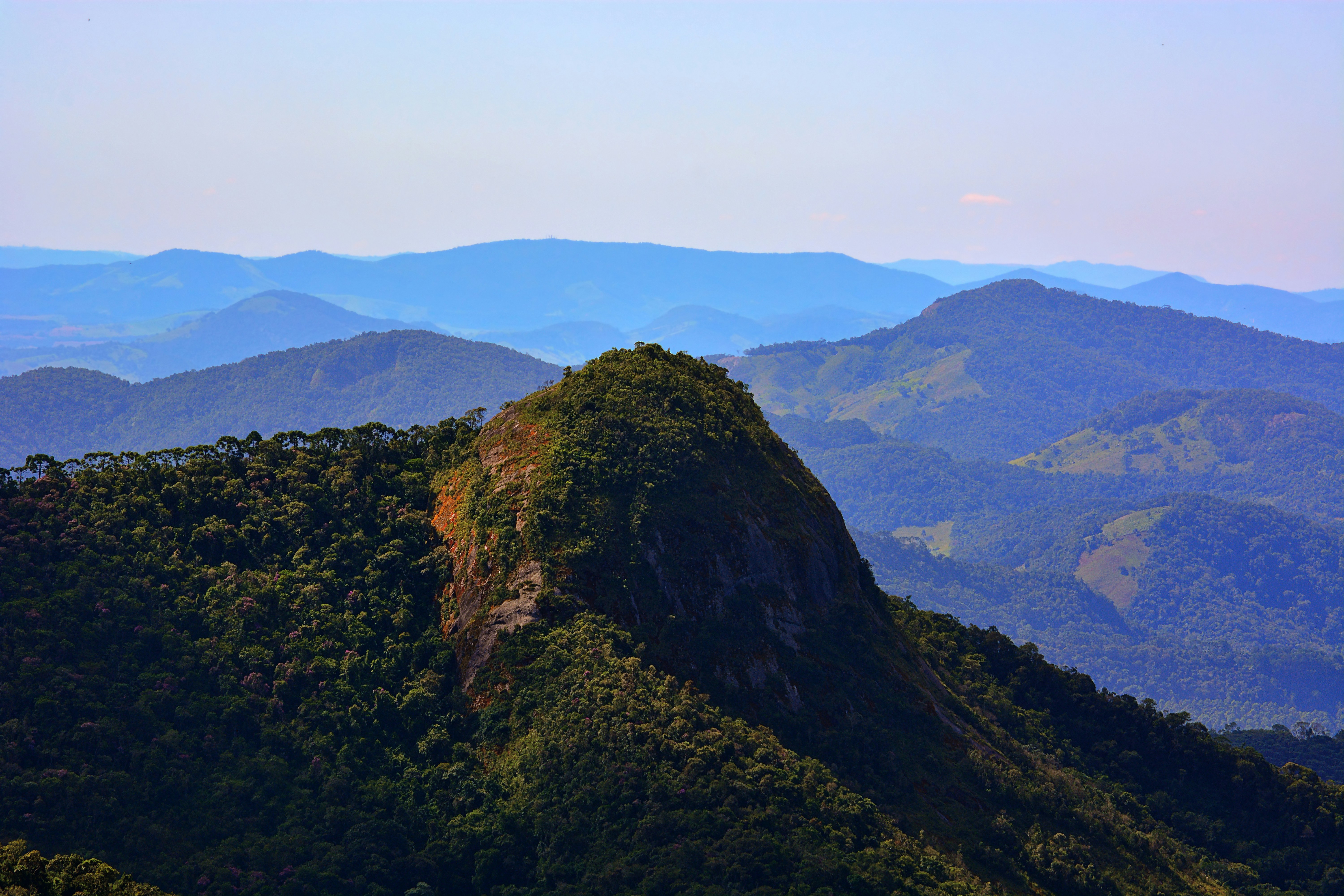 Lush green mountain landscape with rolling hills under a clear blue sky.