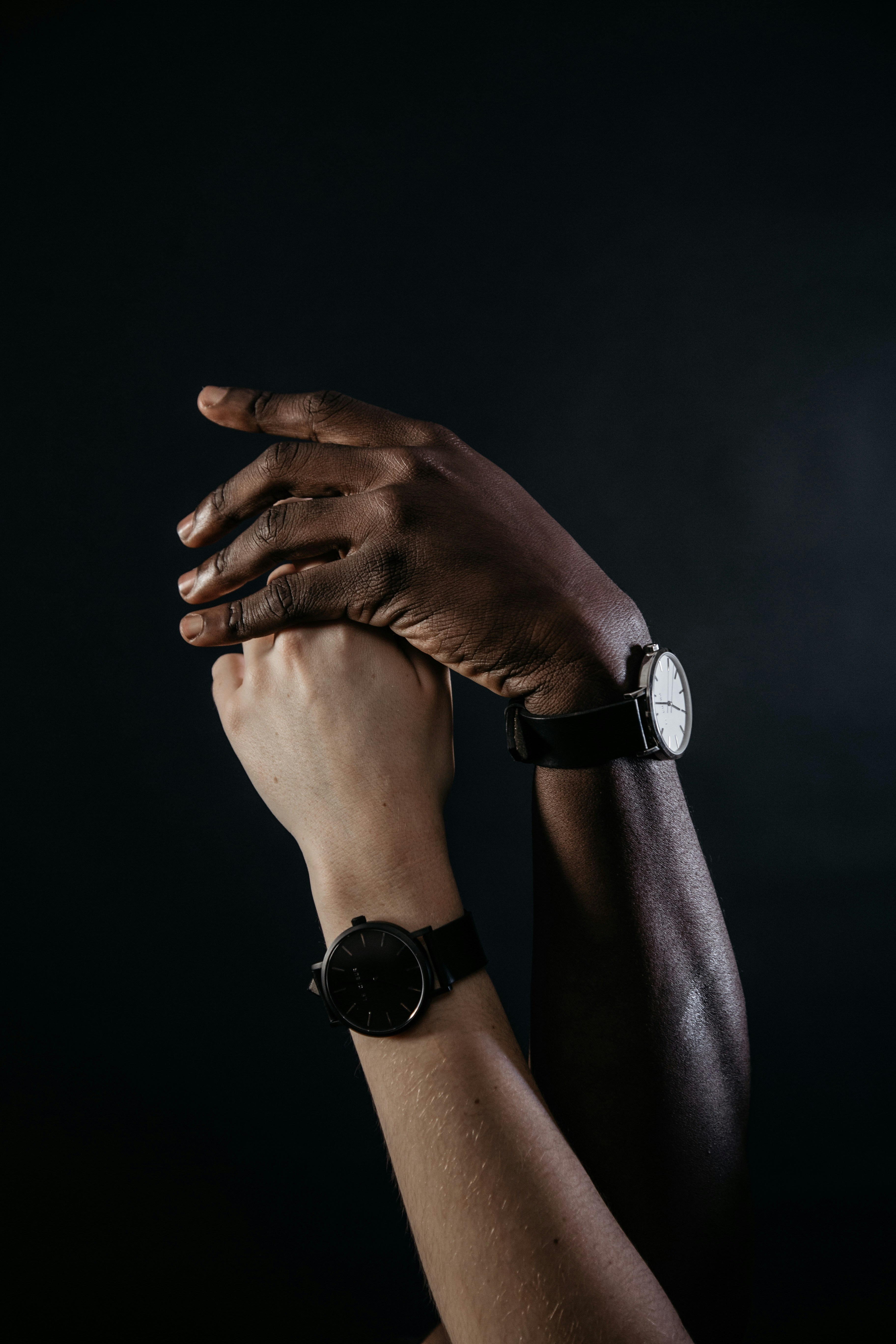 Two hands intertwined, each adorned with distinct watches, set against a dark backdrop.