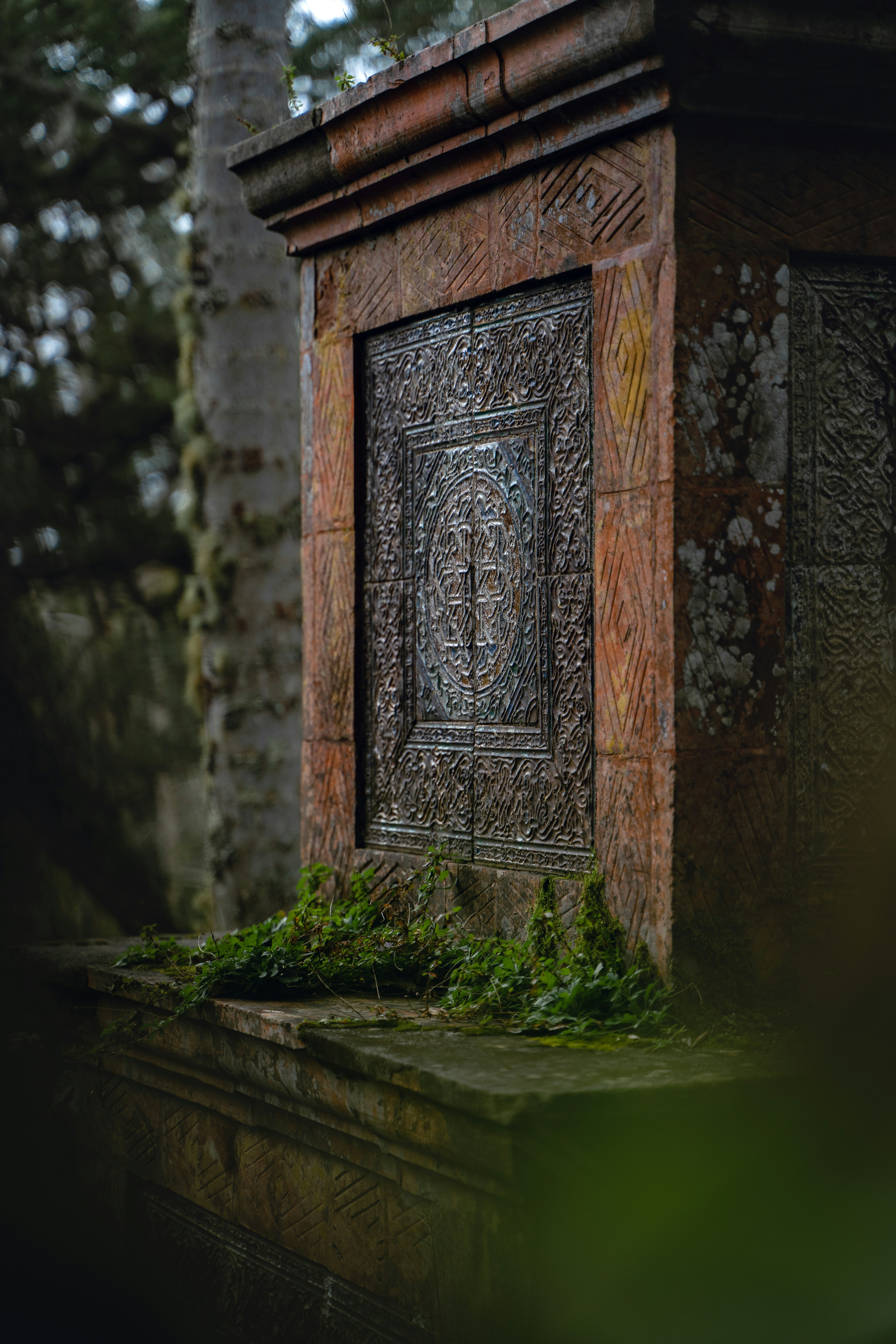Intricate stone relief adorned with nature's touch, enveloped by lush greenery in a serene forest setting.