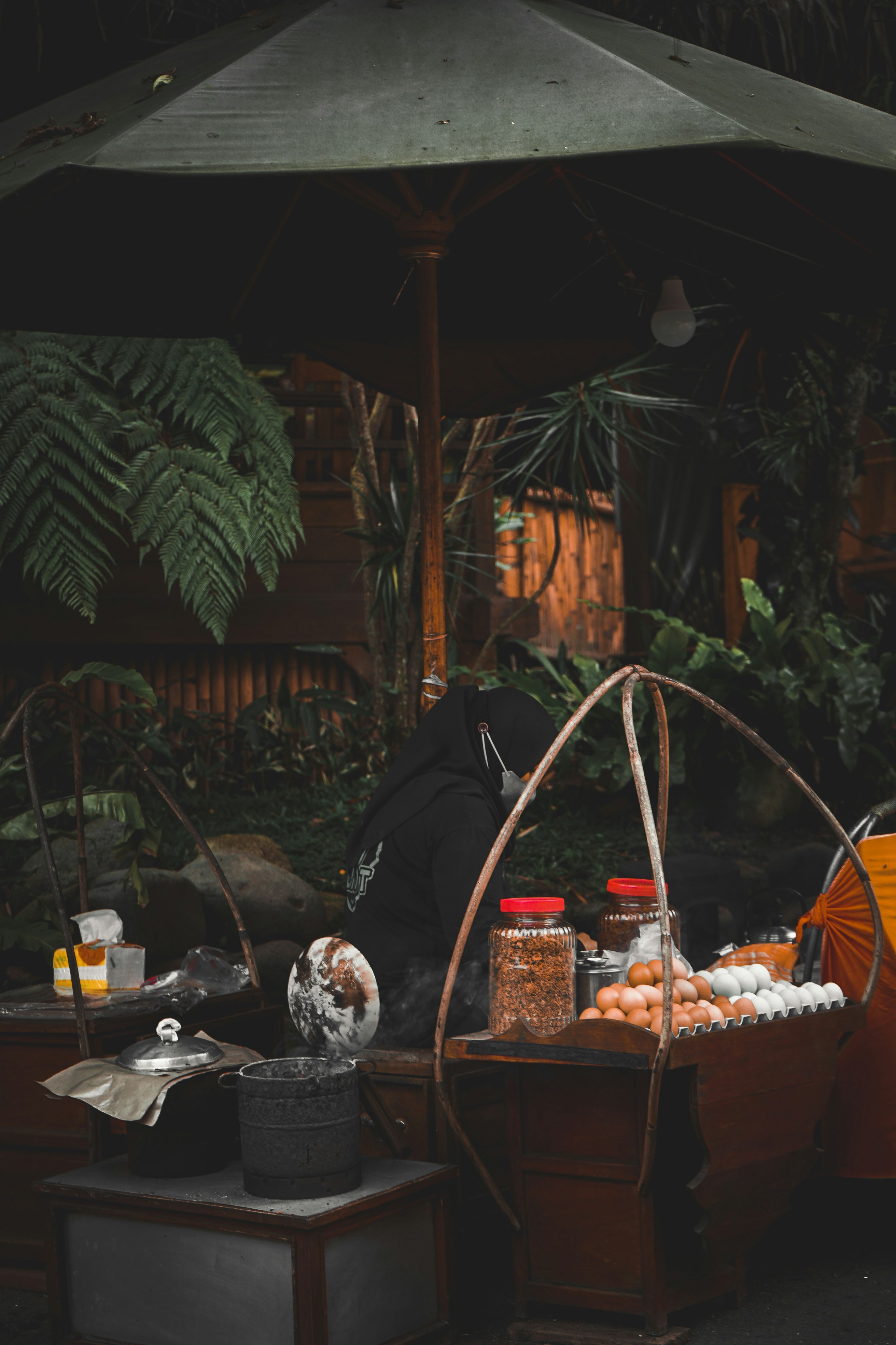 Umbrella Market at Dusk: A Hooded Vendor Tends a Rustic Egg Cart