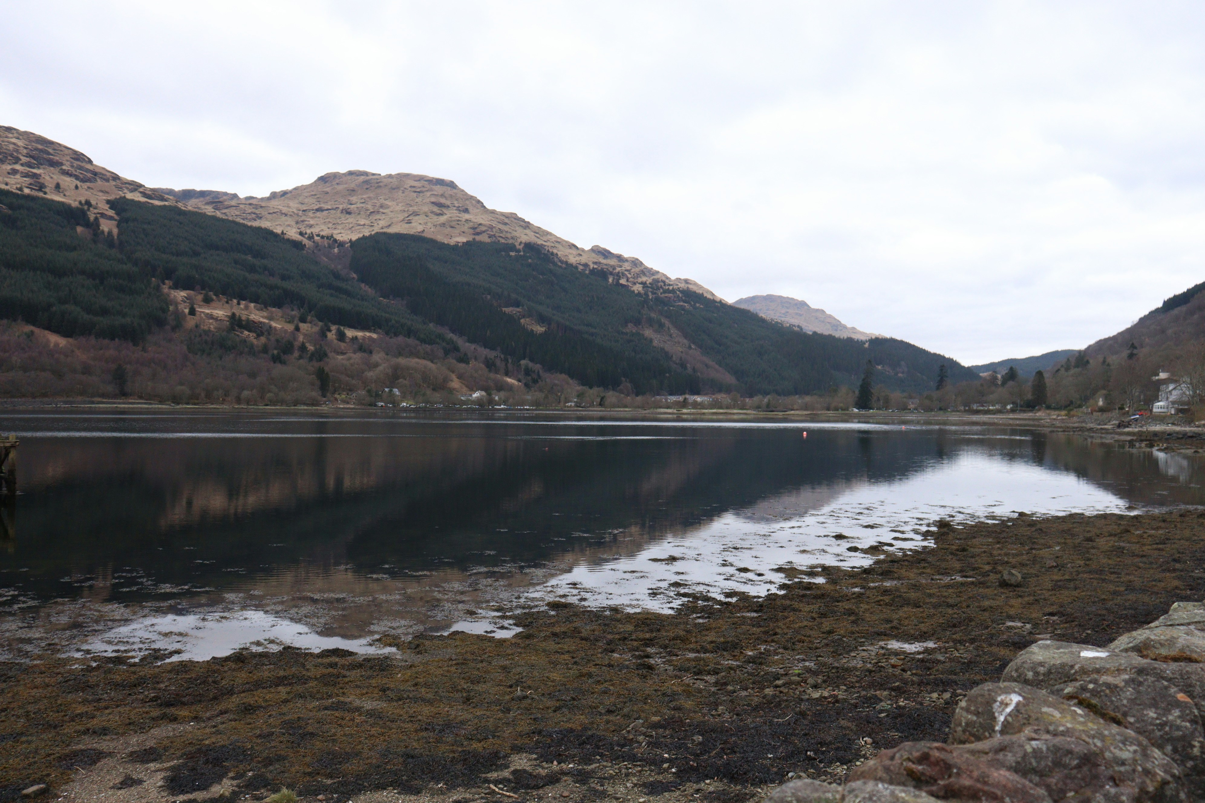 Calm lake mirroring rugged mountains and cloudy sky in a tranquil landscape.