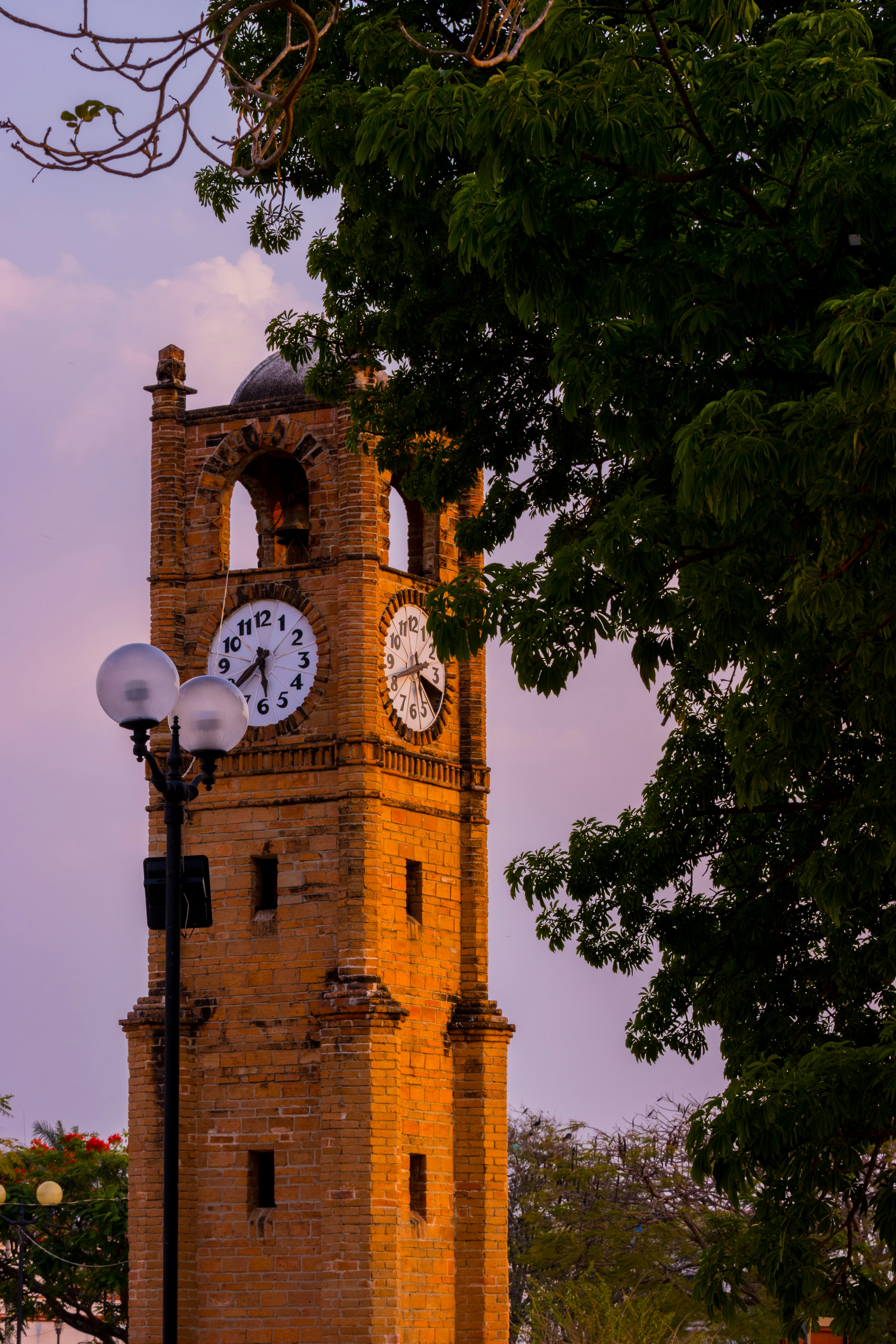 Amber Clock Tower at Dusk, Framed by Lanterns and Foliage