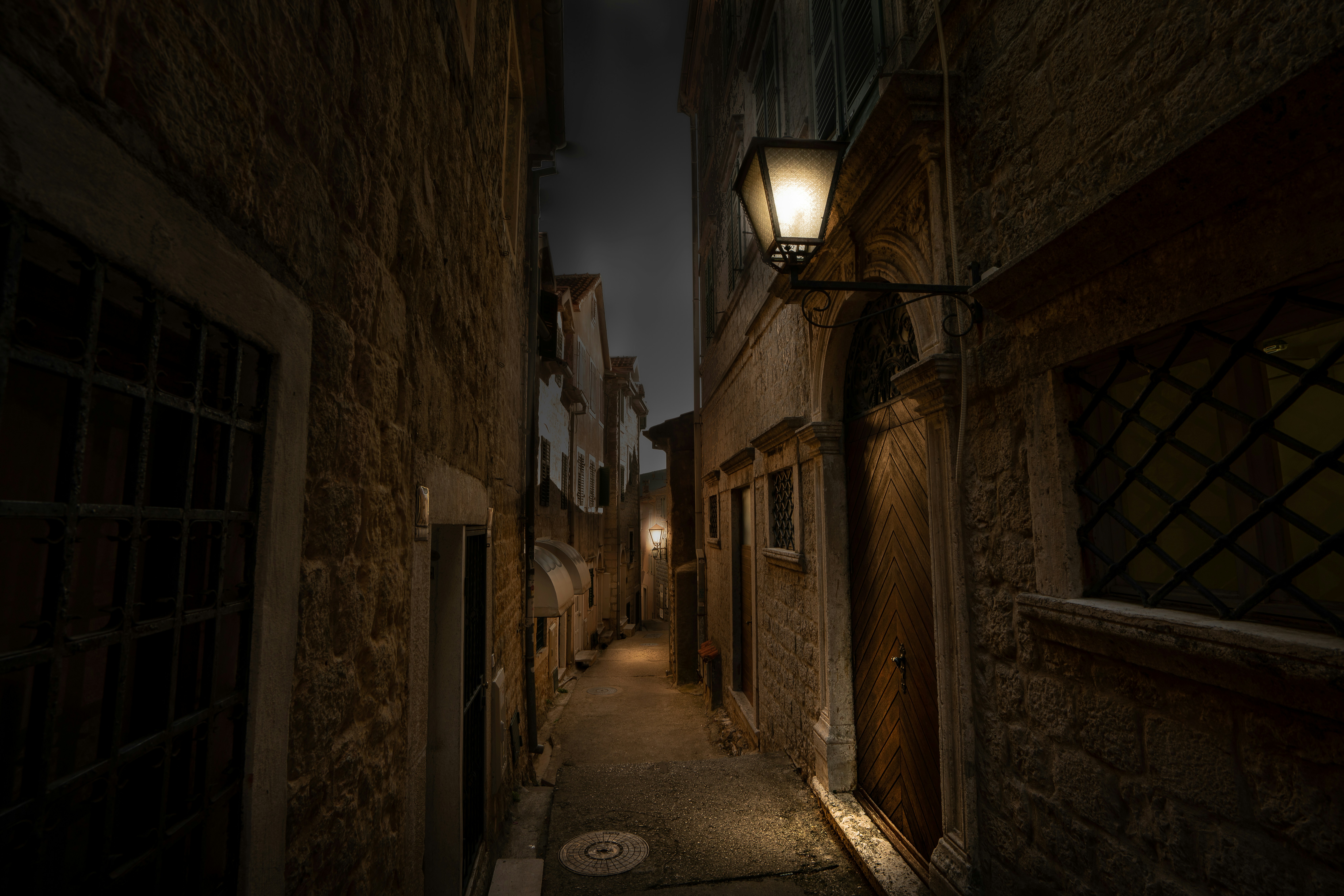 A dark alley with a lamp on the side of it photo – Free Alley Image on ...