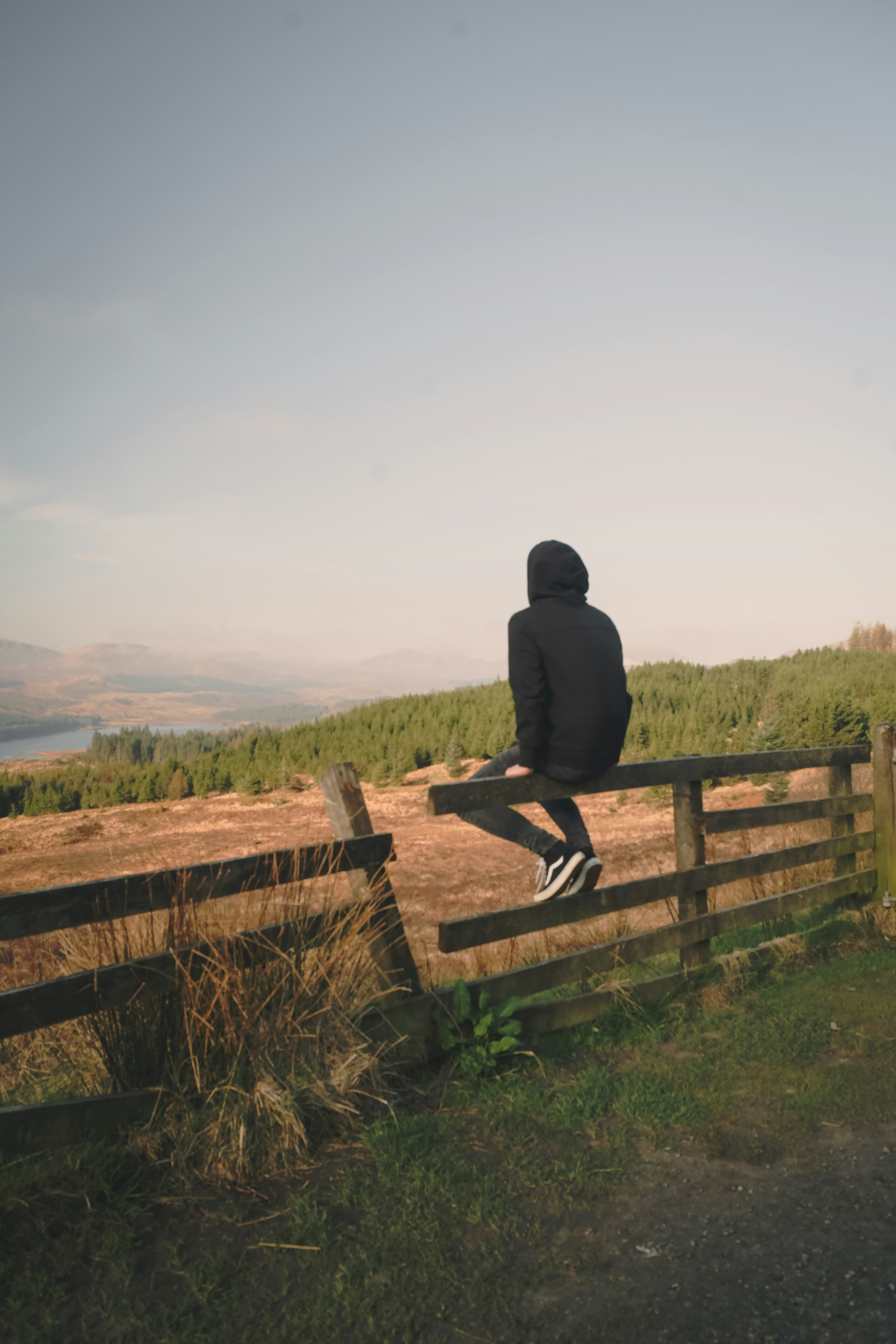 A person sitting on a fence looking over a field photo – Free Grass ...
