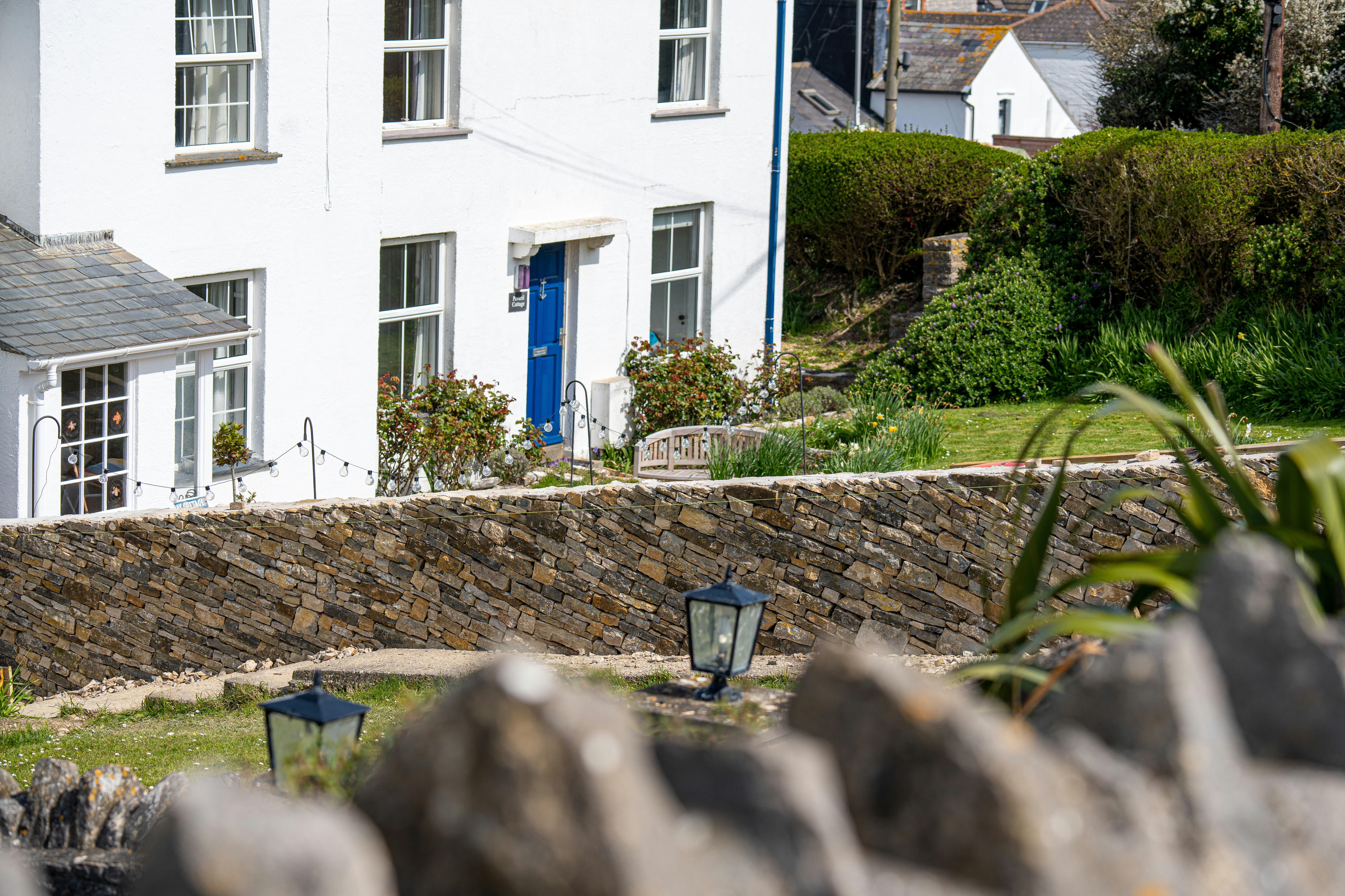 White cottage with blue door framed by stone terrace and garden