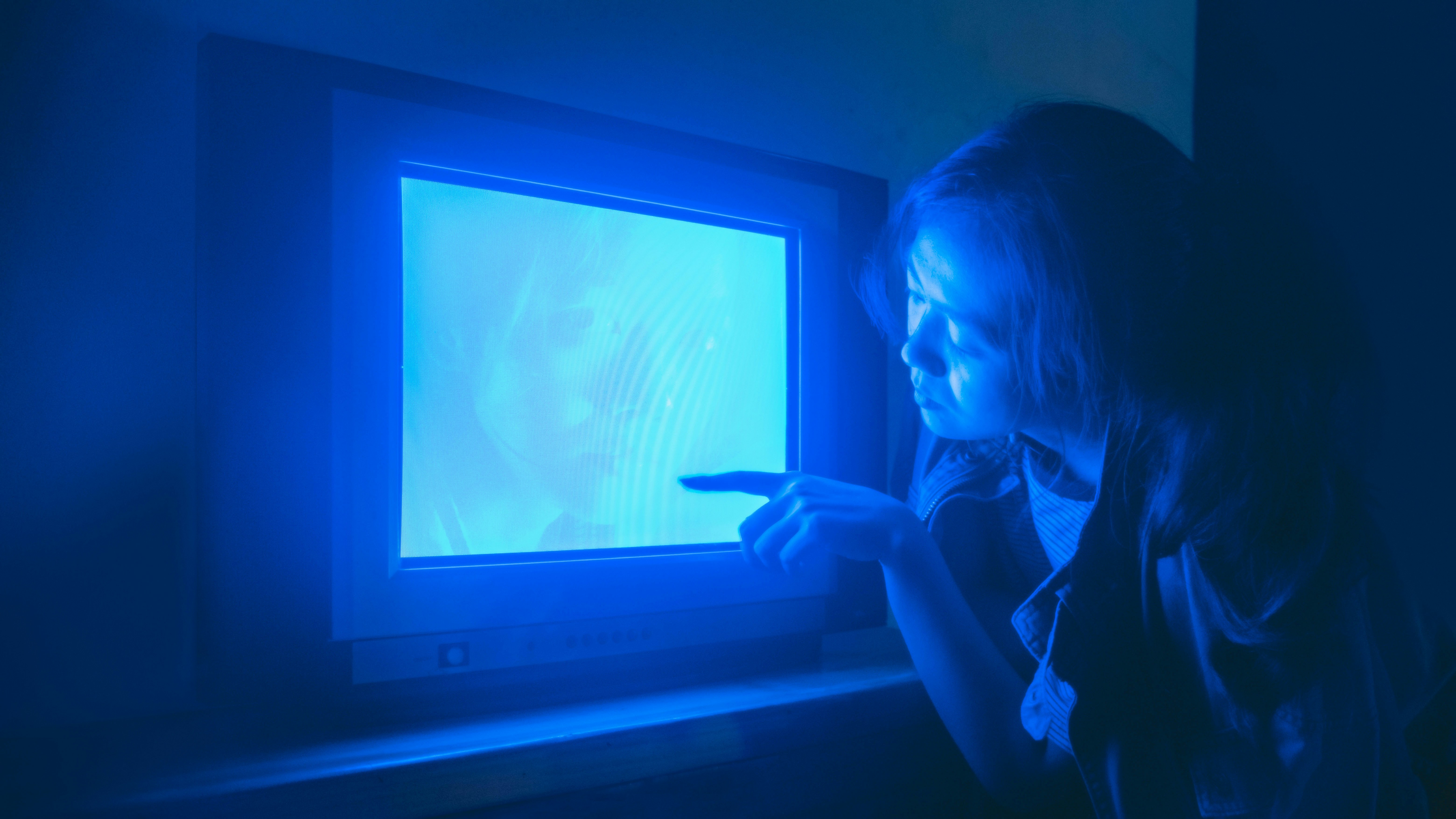 A woman pointing at a television screen in a dark room photo – Free ...